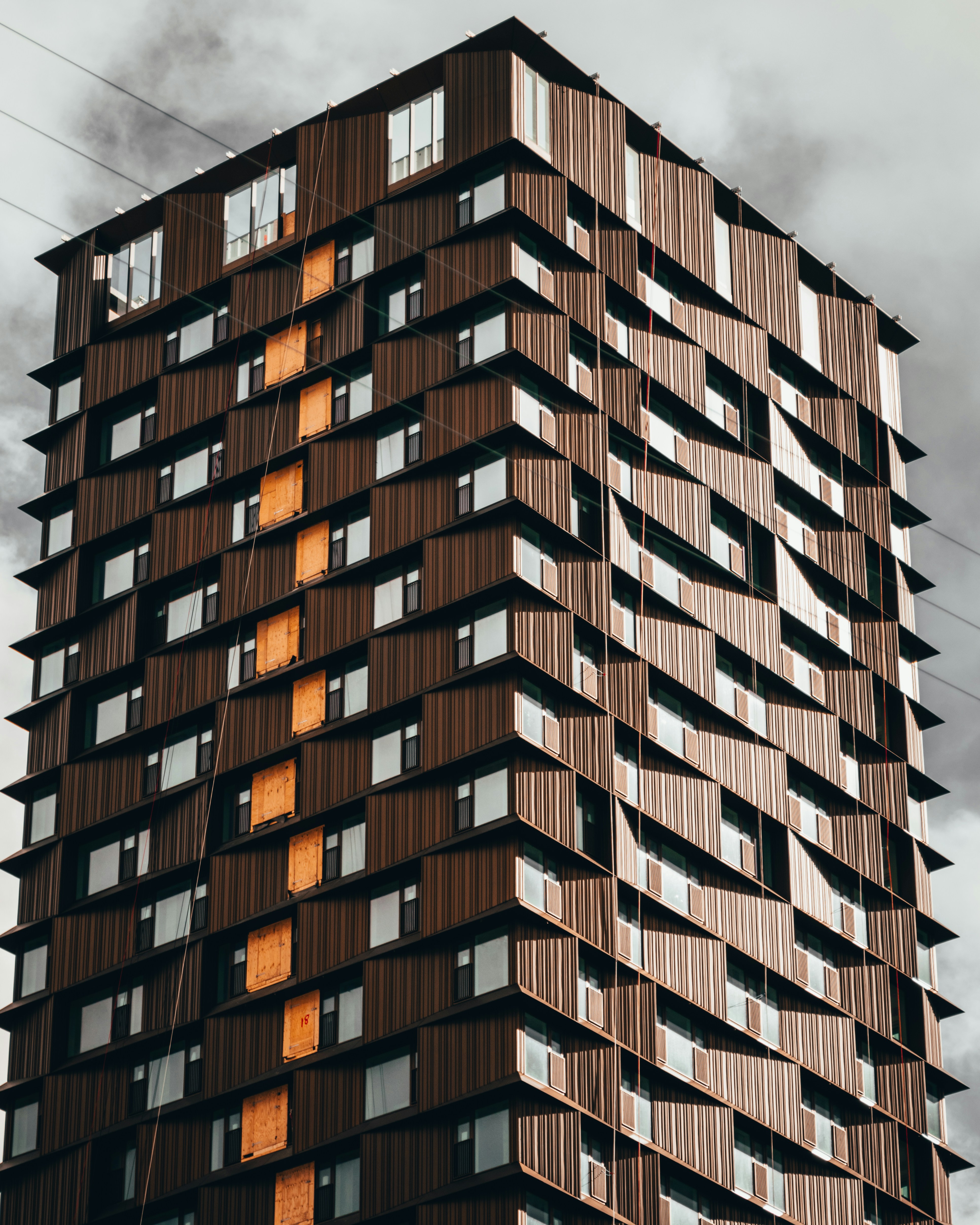 Modern high-rise building with an intricate facade showcasing alternating textures and wooden elements. The structure reflects contemporary architectural design.