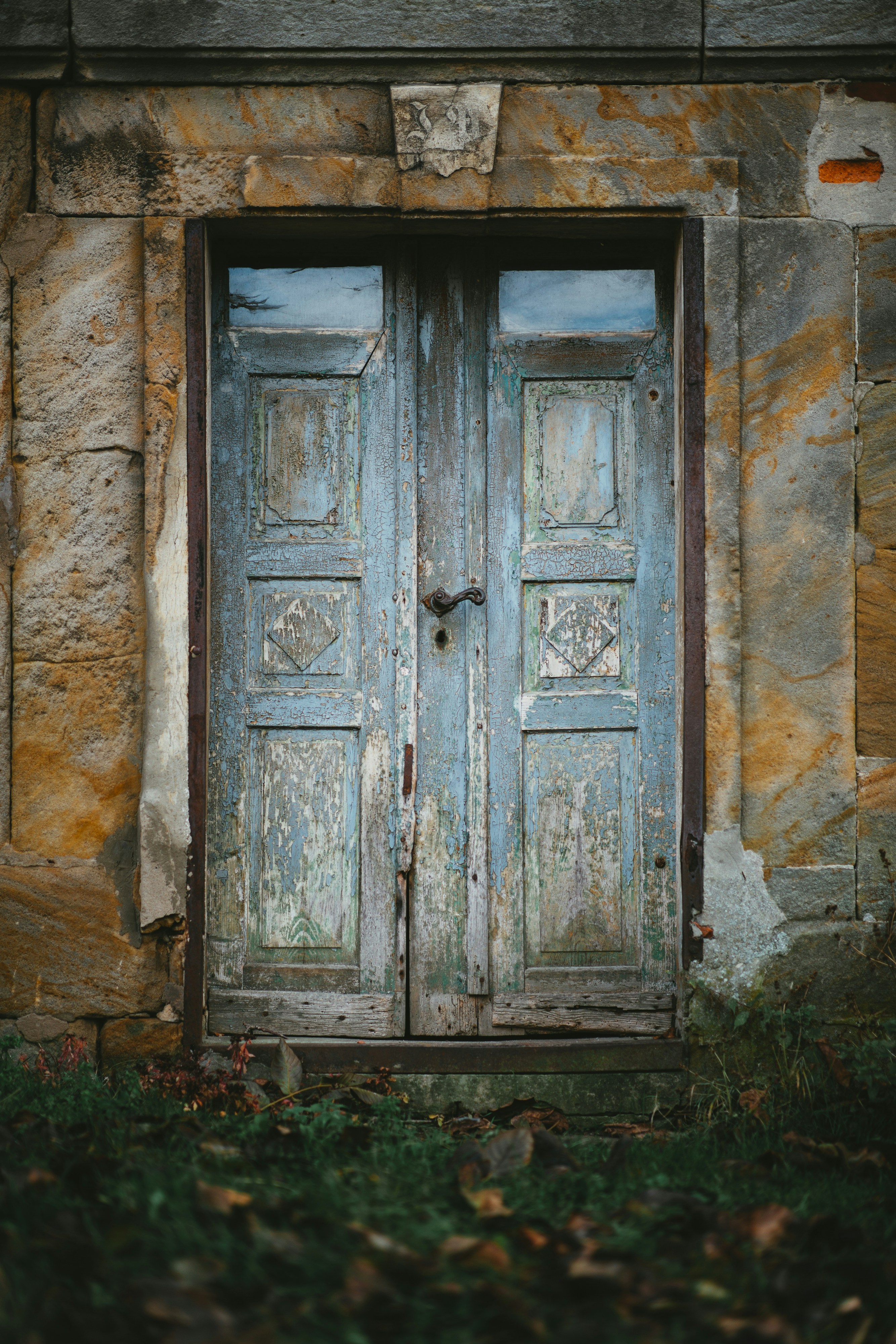 A weathered blue door with peeling paint set against a rustic stone wall, evoking a sense of history and mystery.