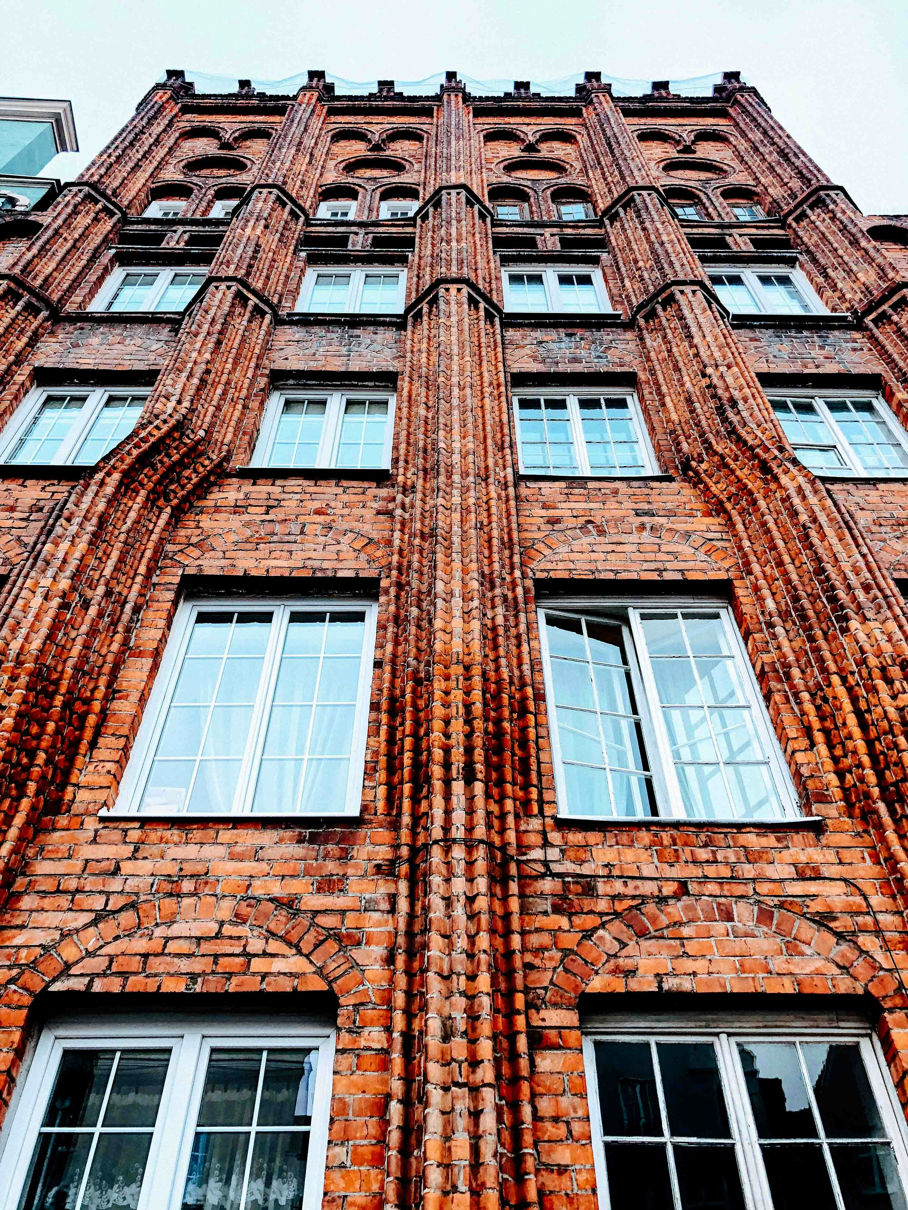 Intricate brickwork and large windows characterize this historic building's facade, showcasing a blend of craftsmanship and design. The perspective emphasizes the verticality and details of the structure.