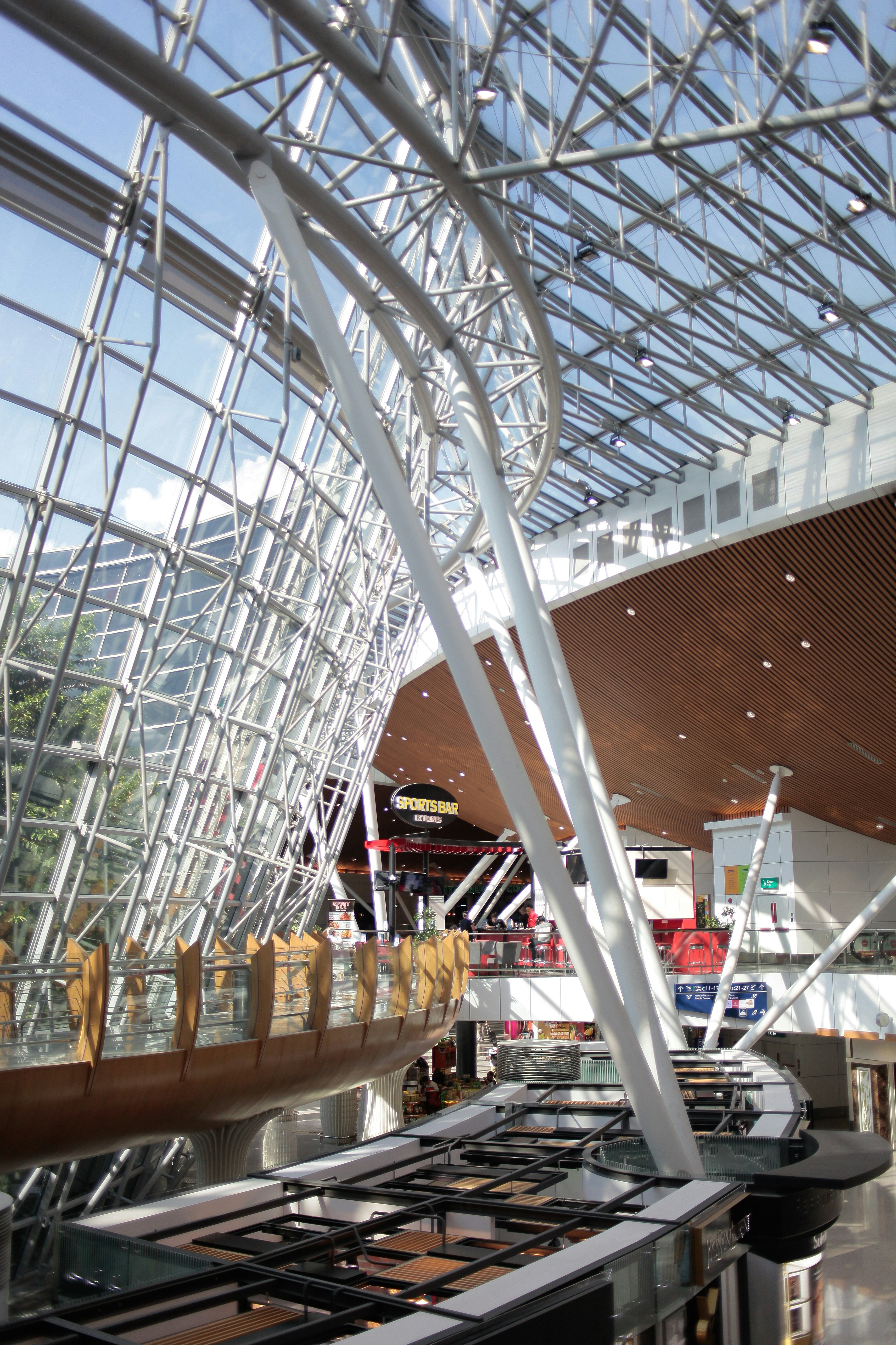 Modern atrium showcasing a blend of glass and wood elements, with intricate steel supports. The design emphasizes an open, airy atmosphere.