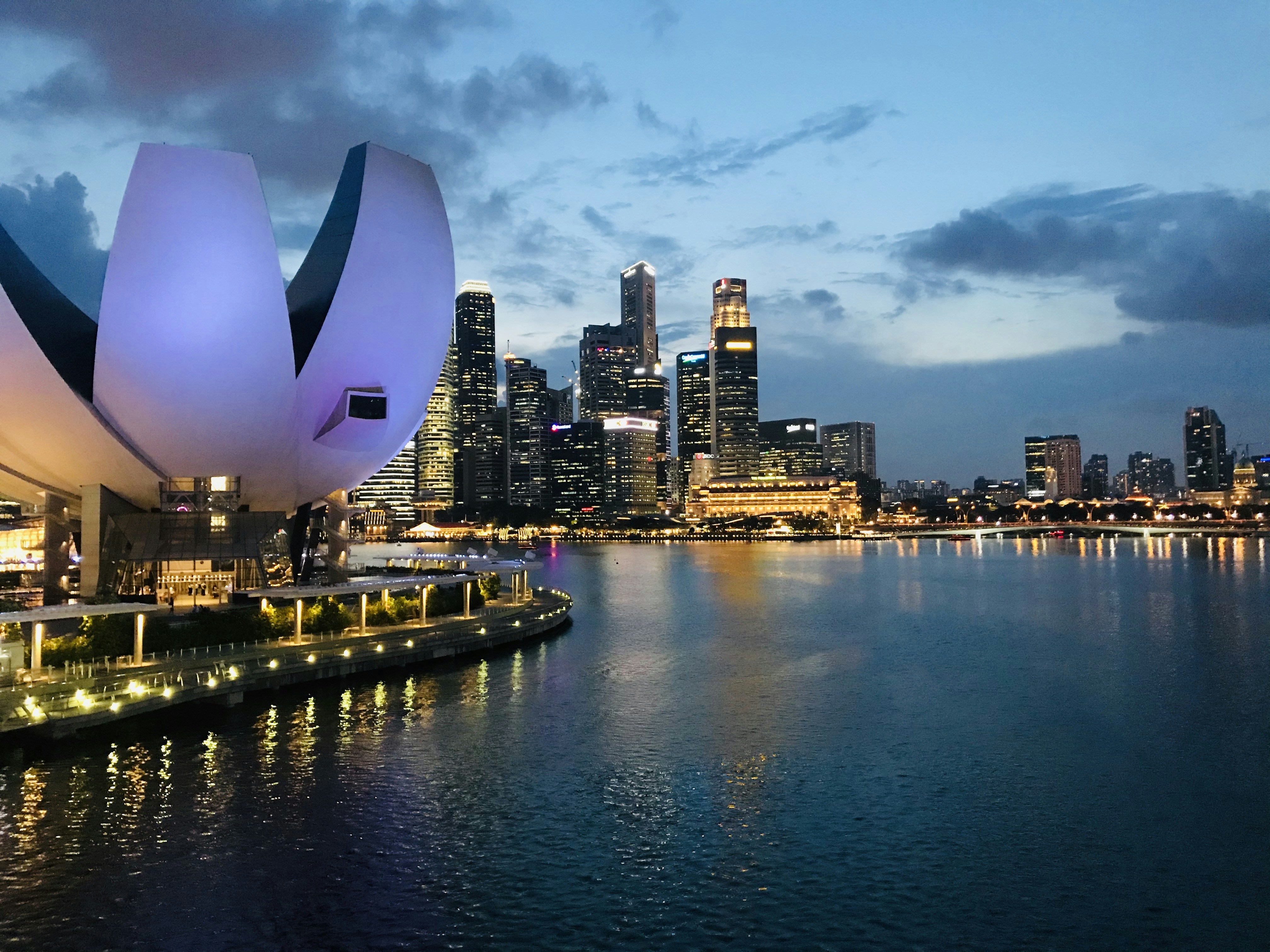 The iconic lotus-shaped structure contrasts with the vibrant skyline of Singapore, reflecting on the calm waters during twilight.