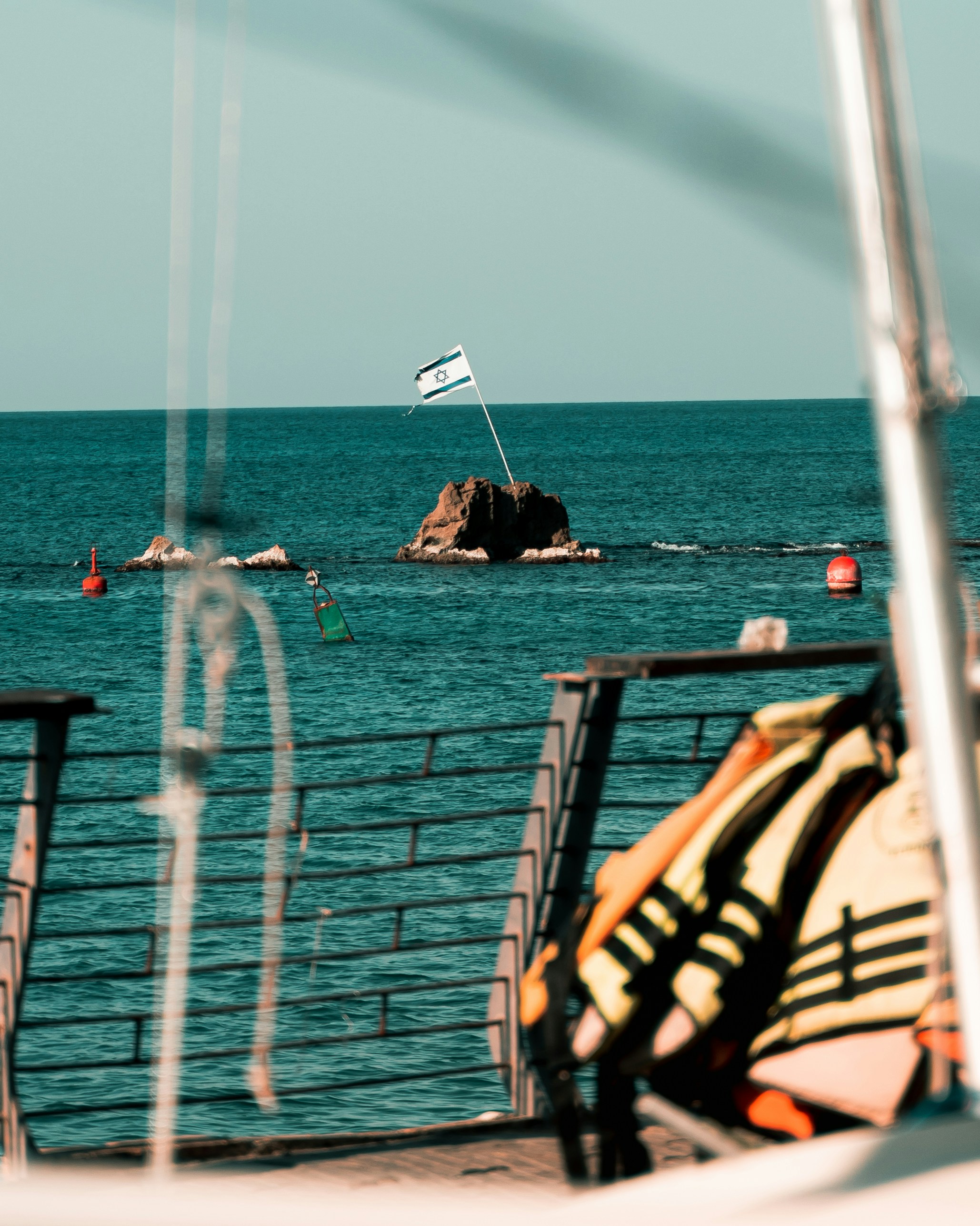 Flag on a Sea Rock: A Quiet Harbor Scene Framed by Sail Mast and Deck Rail