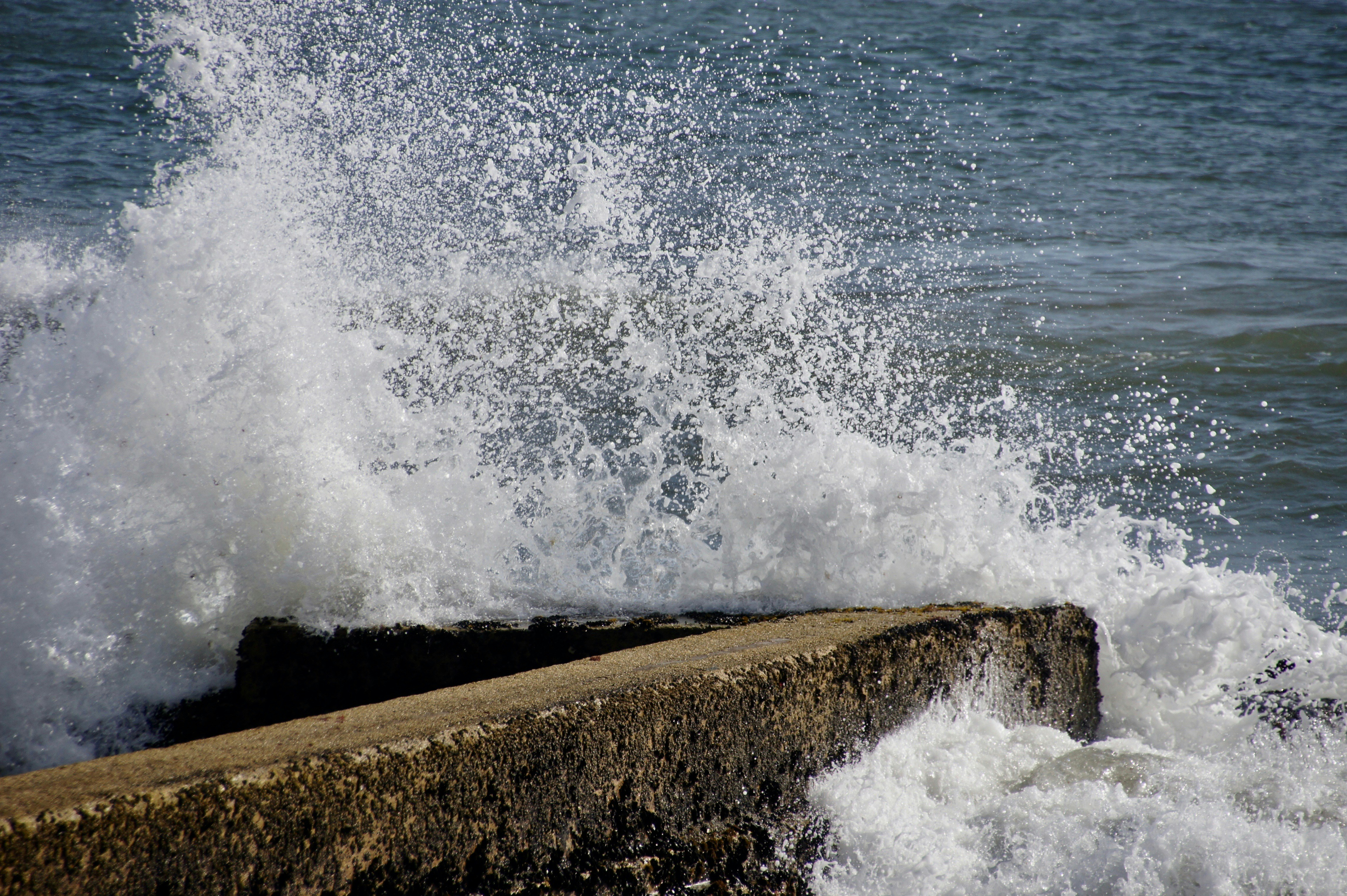 Powerful ocean waves crash against a weathered pier, sending sprays of water into the air. The scene captures the intensity of nature's forces.