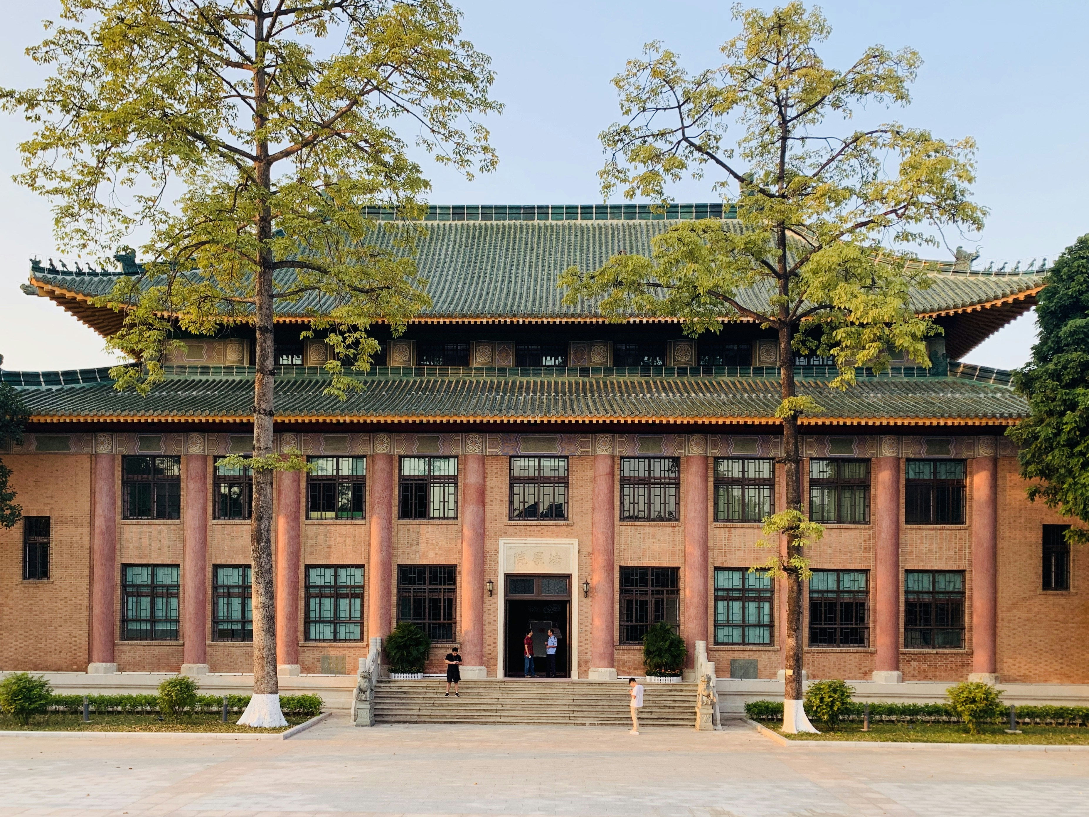 Symmetrical Brick Campus Hall Framed by Tall Trees Under a Green Roof