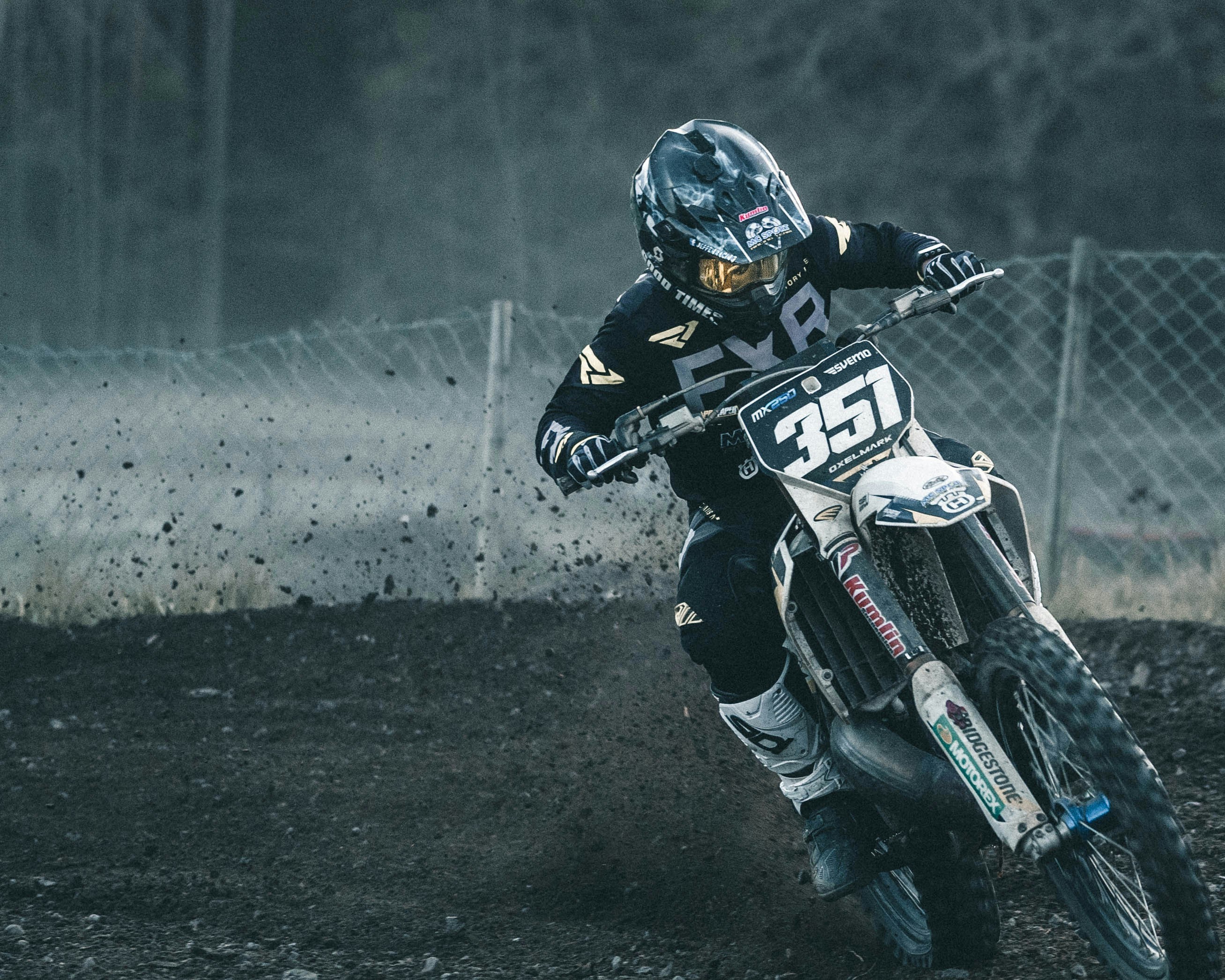 Motocross rider expertly navigating a dirt track, sending up clouds of dust and showcasing skillful control. The scene captures the thrill of off-road racing.