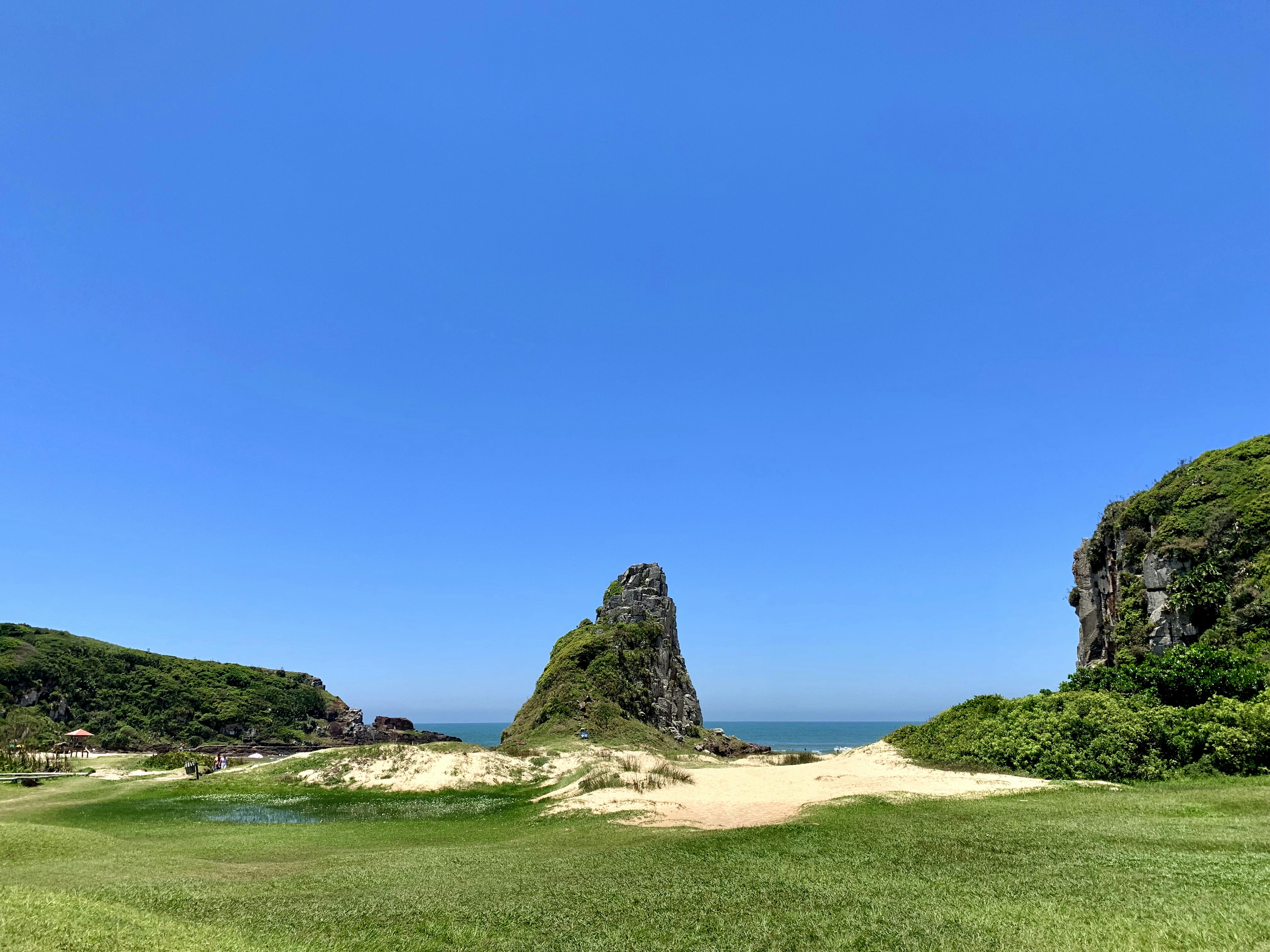 Verdant landscape with a prominent rock formation under a clear blue sky.