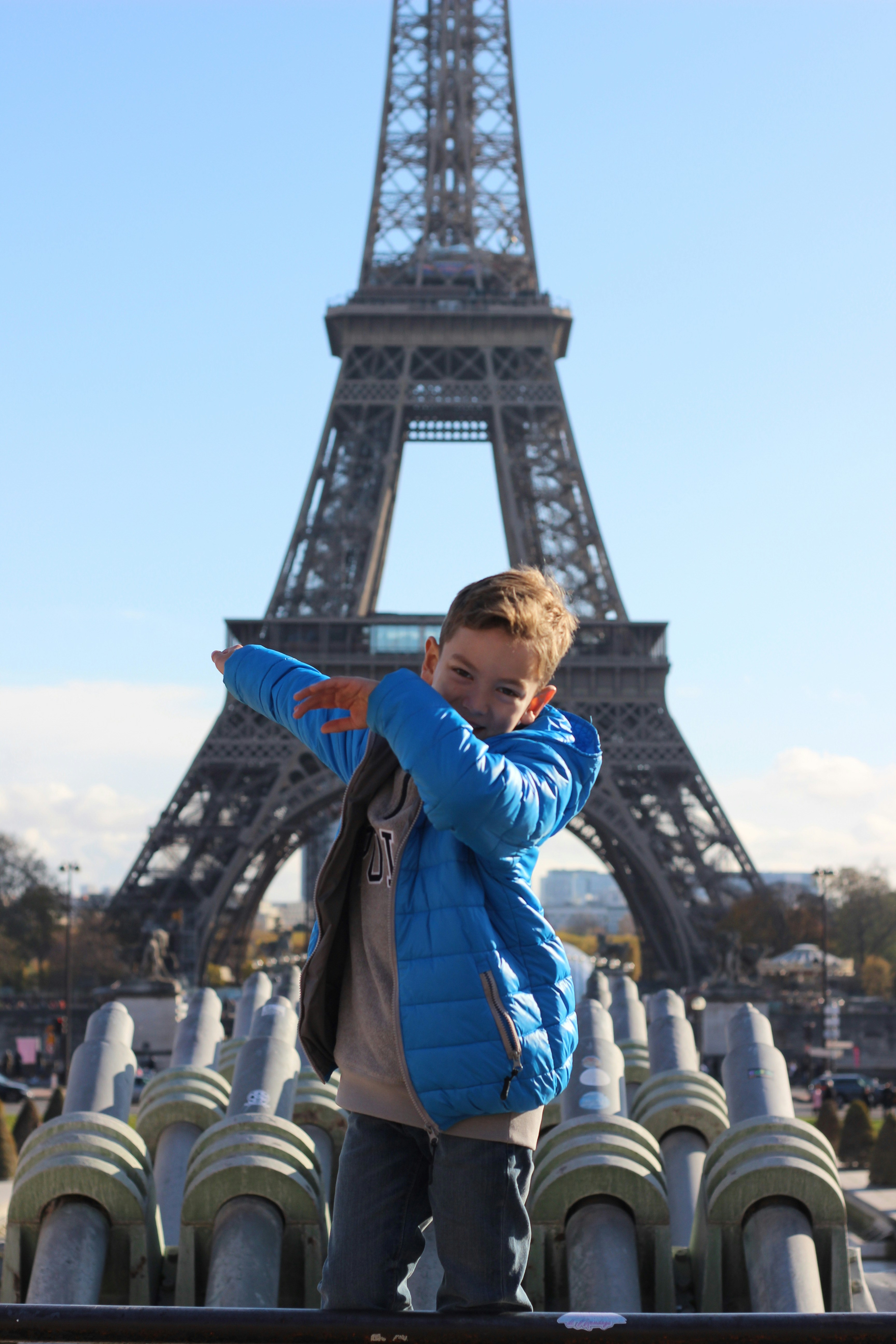 Child in a blue jacket dashes in front of the Eiffel Tower