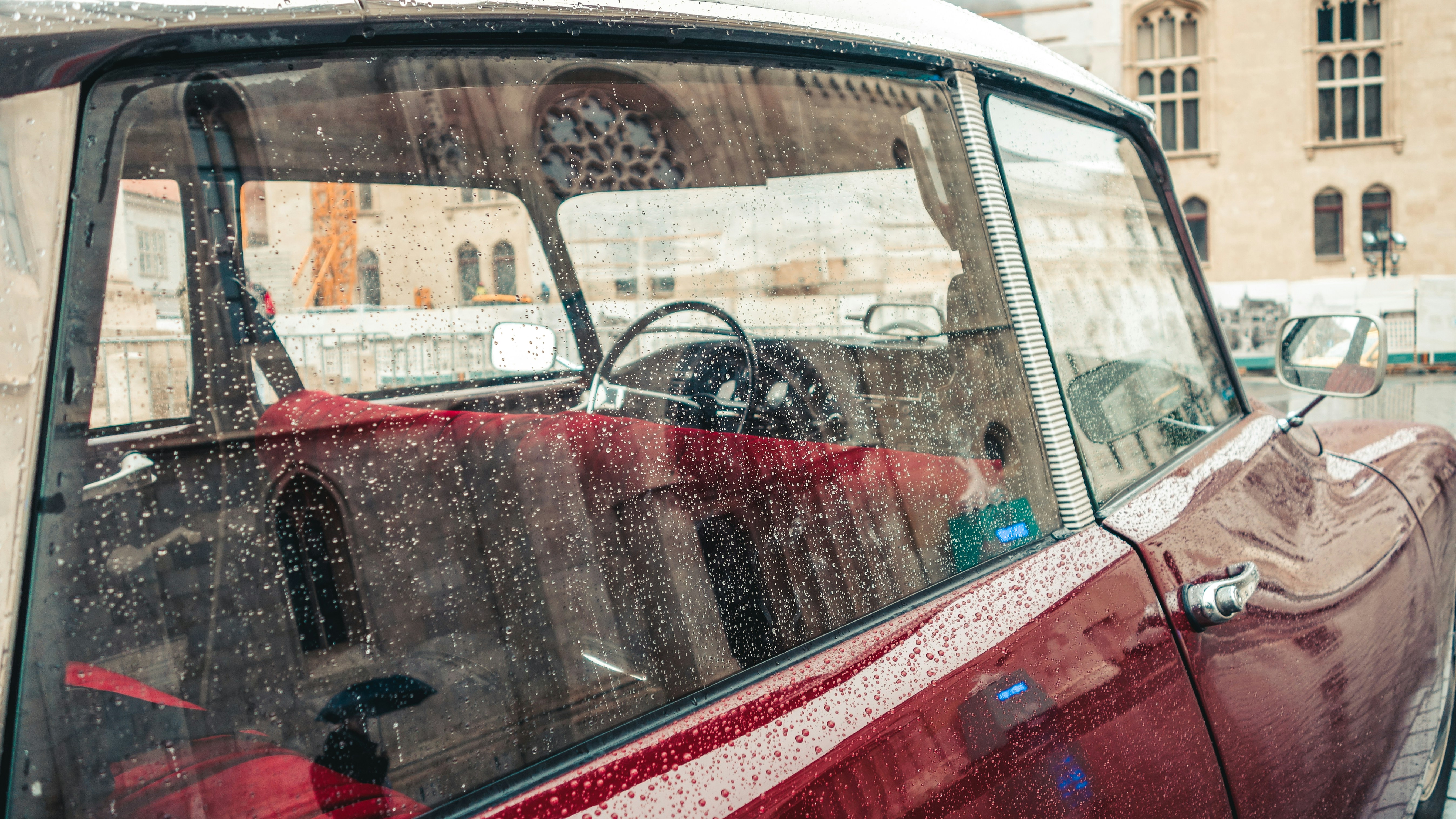 Rain-kissed vintage red convertible beside a historic stone facade