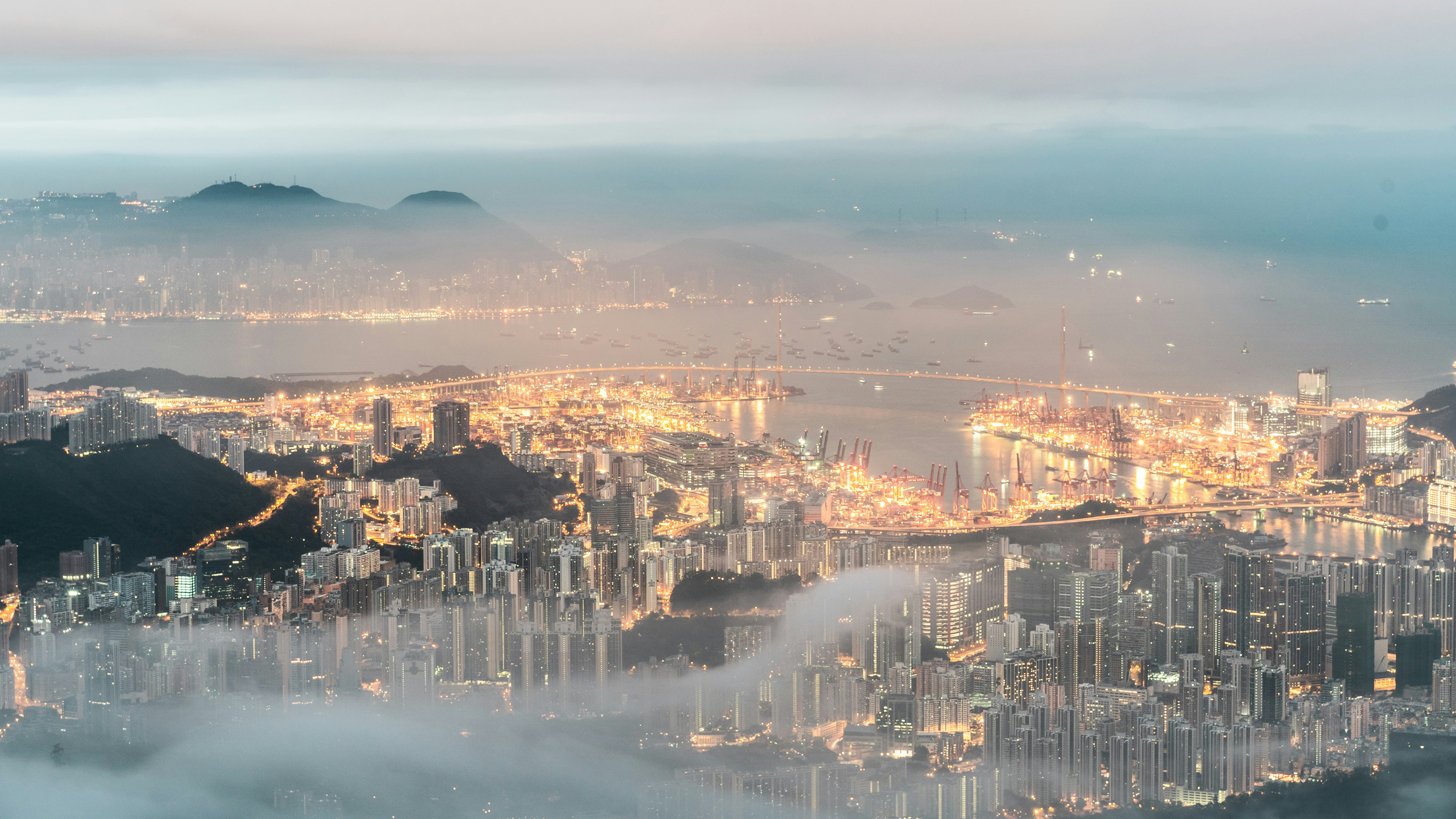Cityscape with illuminated buildings and bridges enveloped in early morning fog.