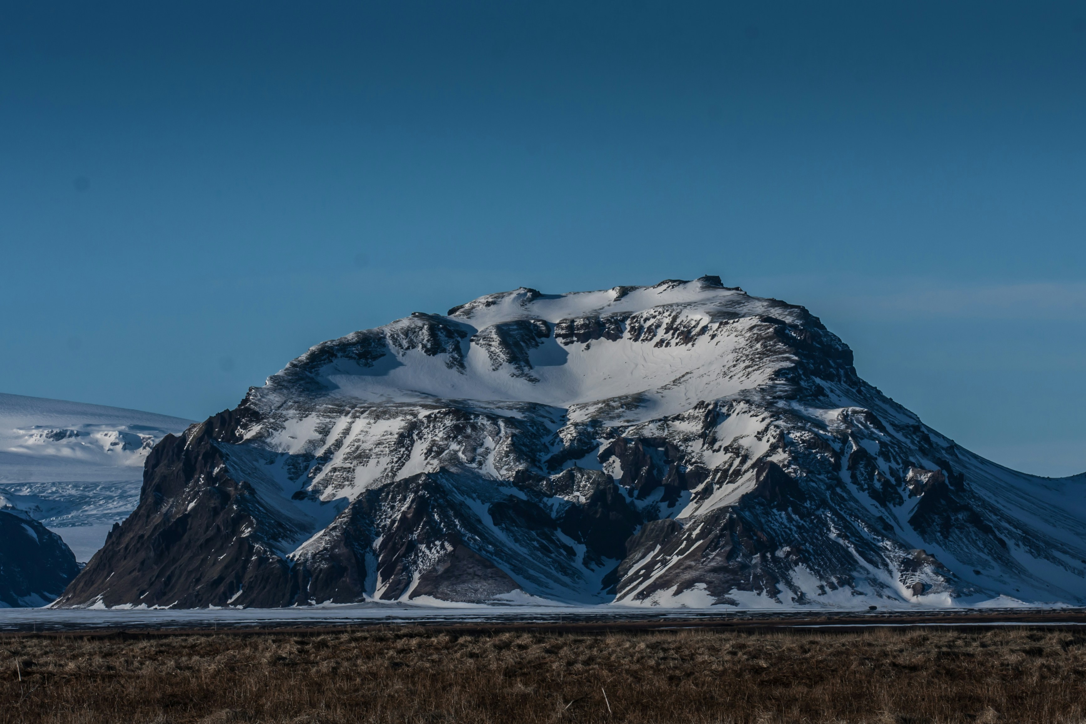 A rugged mountain crowned with snow against a clear blue sky, showcasing the stark beauty of a remote landscape.