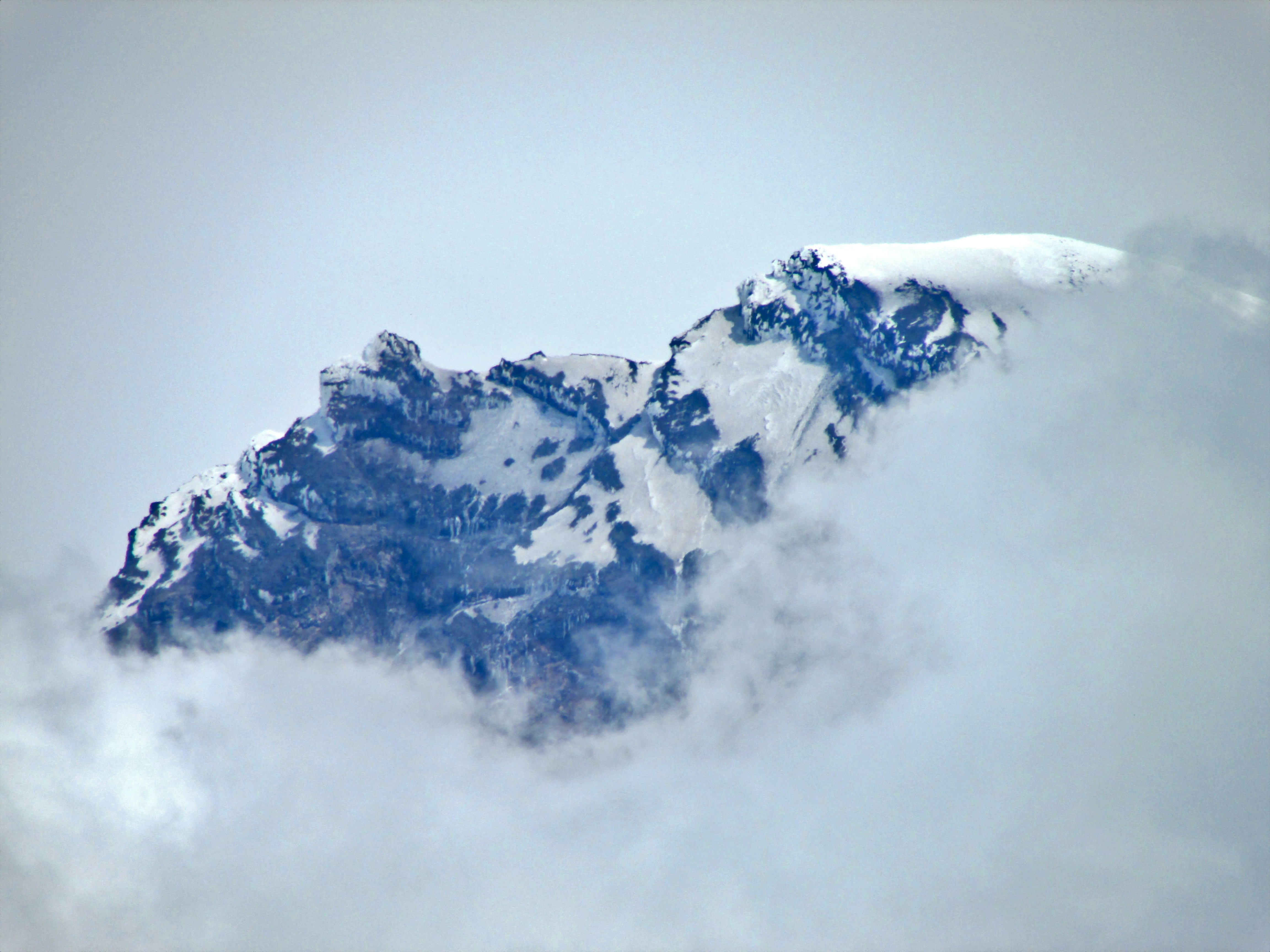 Snow-capped mountain peak partially shrouded in clouds, showcasing rugged terrain and high-altitude beauty.