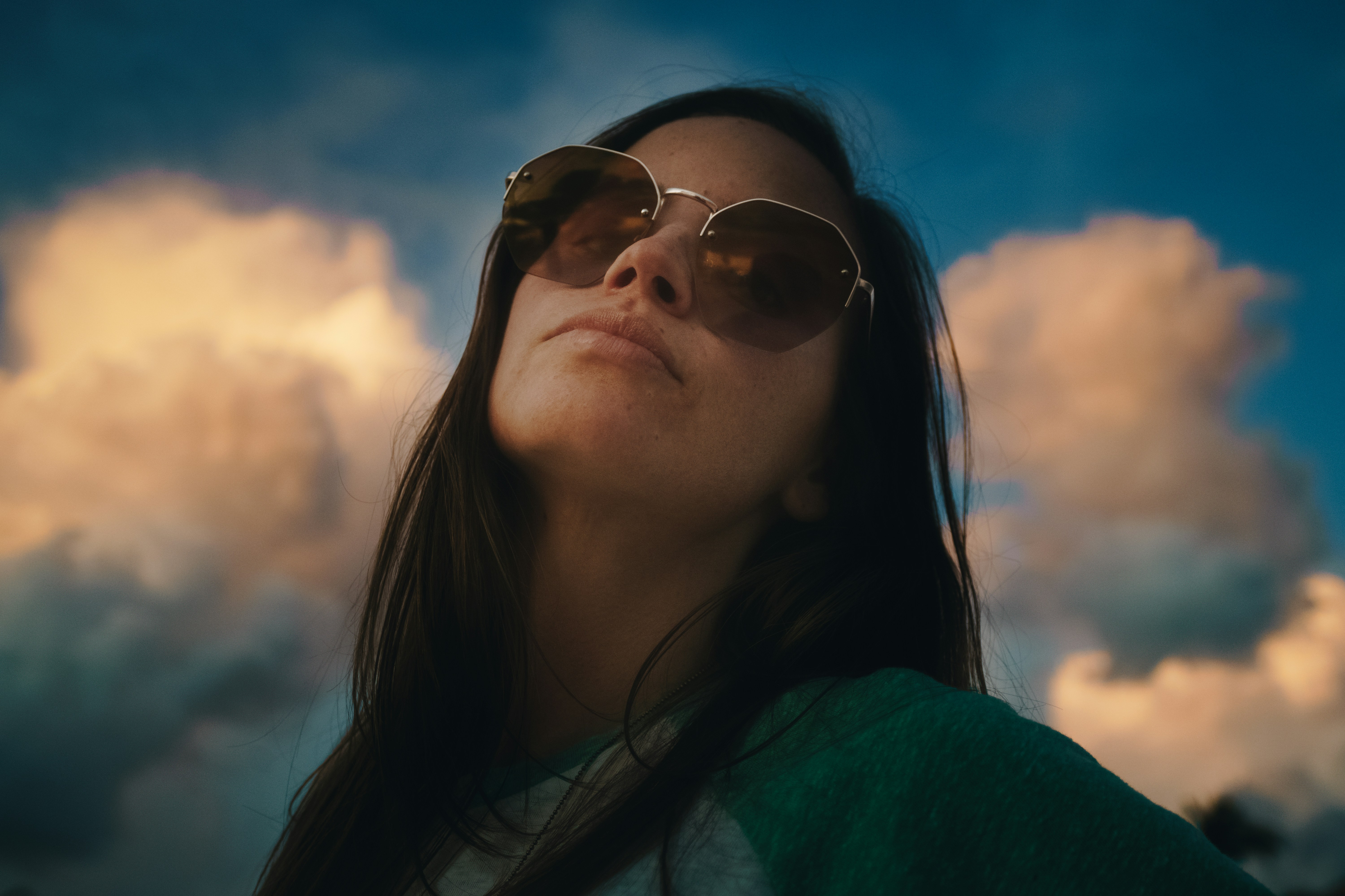 Person in gold-framed sunglasses gazing upwards with dramatic clouds in the background.