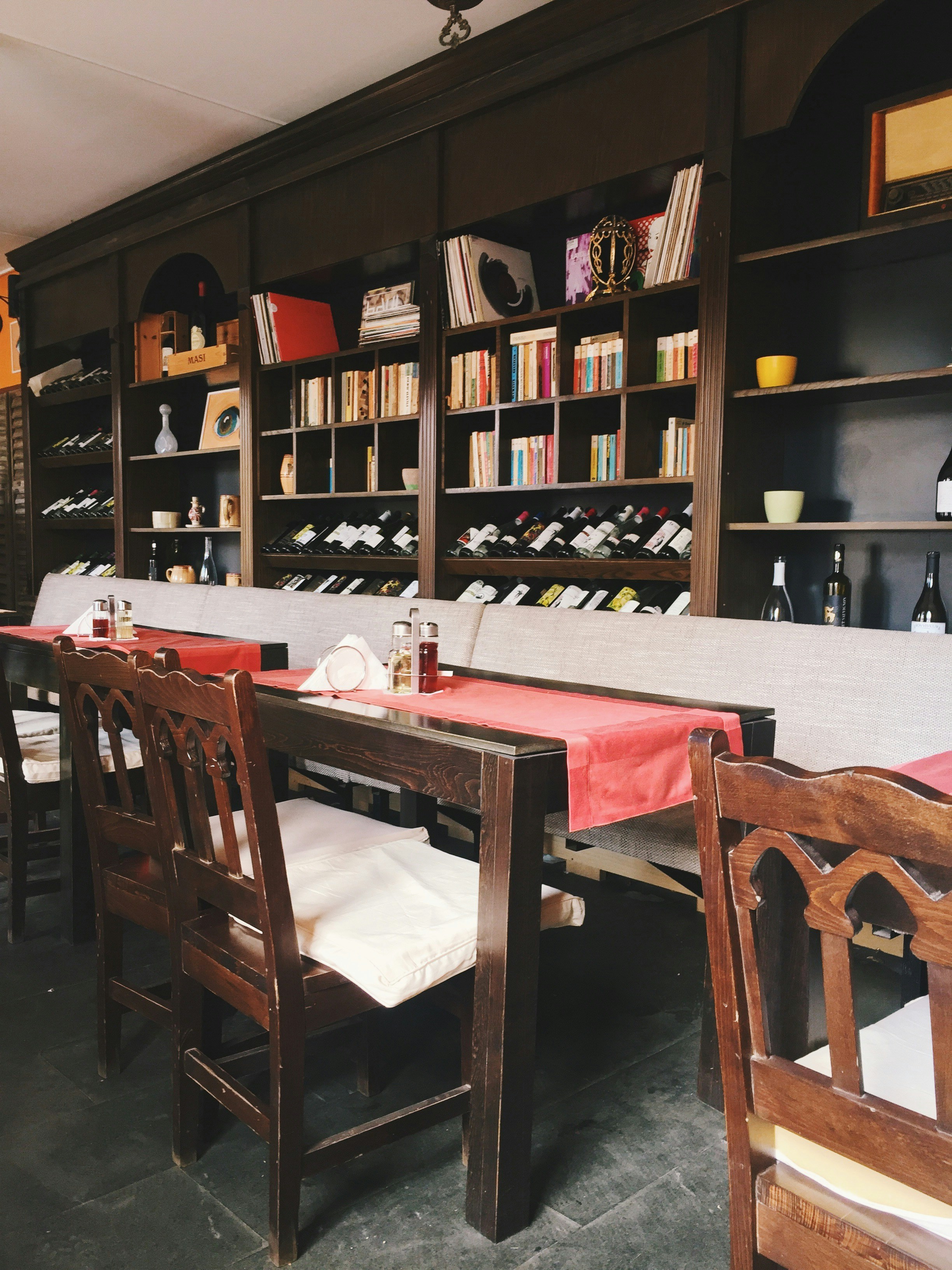 Warm wooden tables set against a backdrop of shelves filled with books and wine bottles in a quaint restaurant.