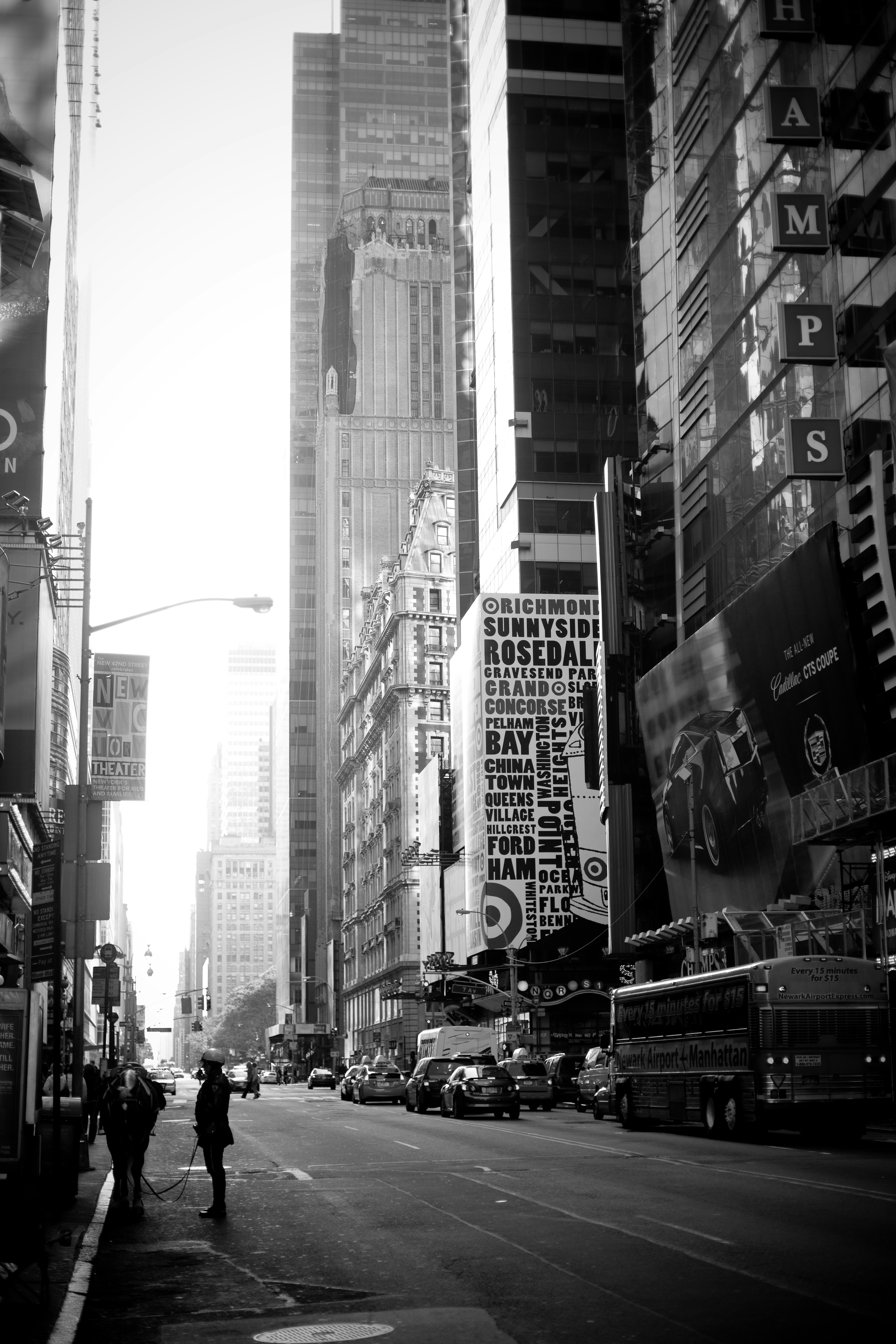 Black and white street scene capturing pedestrians and towering skyscrapers in a bustling city. Billboards and signs add a historical touch to the urban landscape.