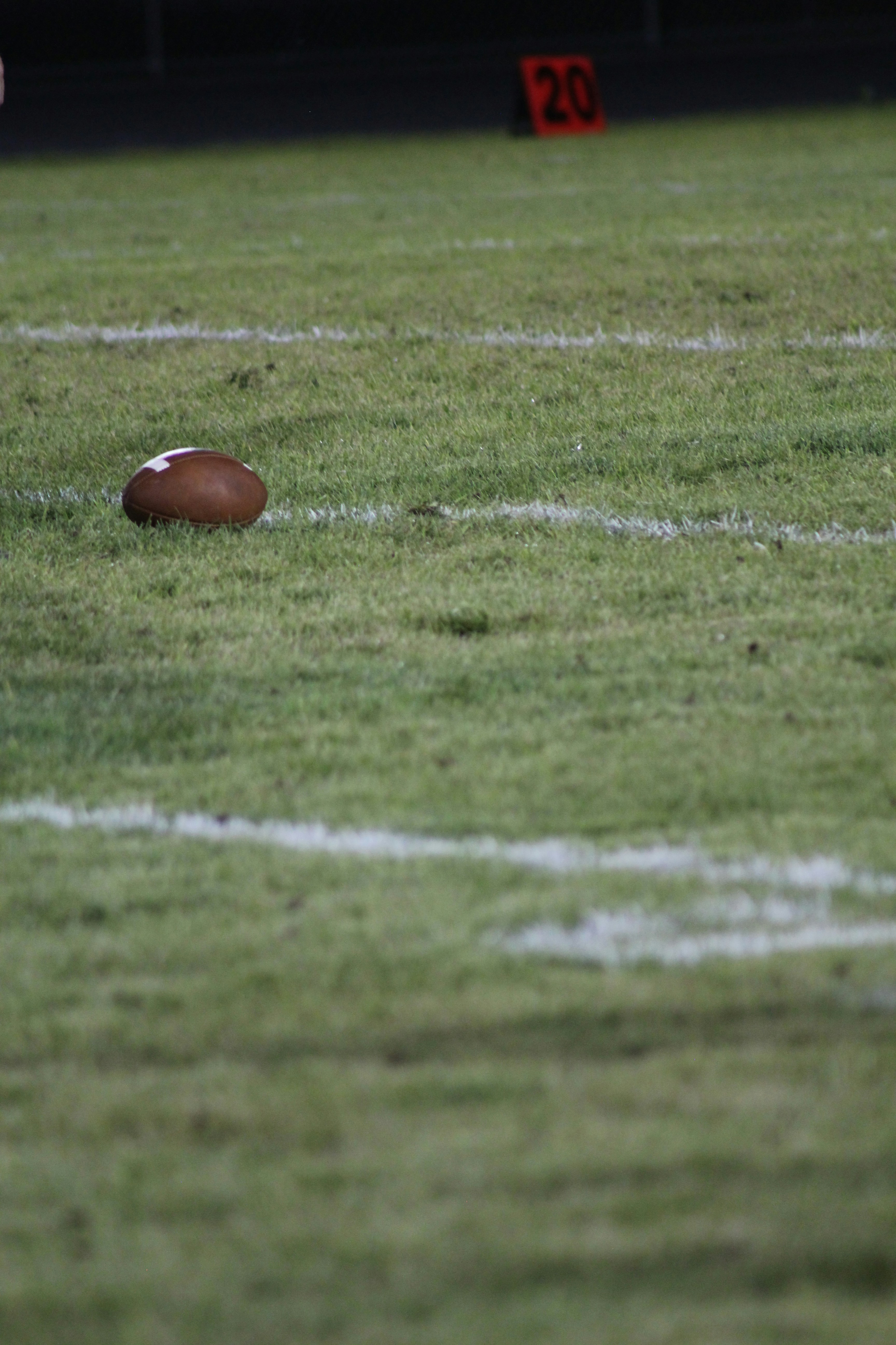 Lone football on a grass gridiron under dim stadium light