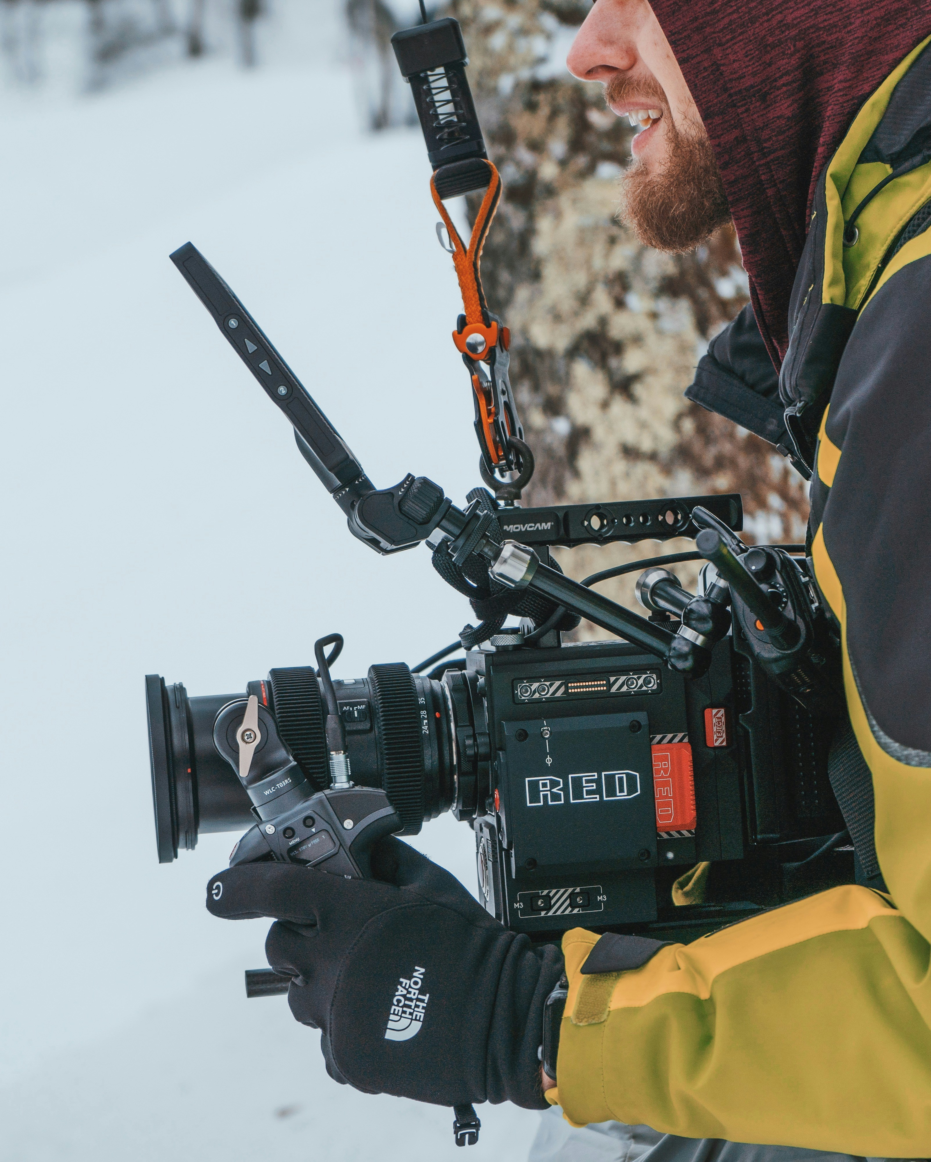 Cameraman in winter attire operates a RED camera while capturing footage in a snowy landscape.