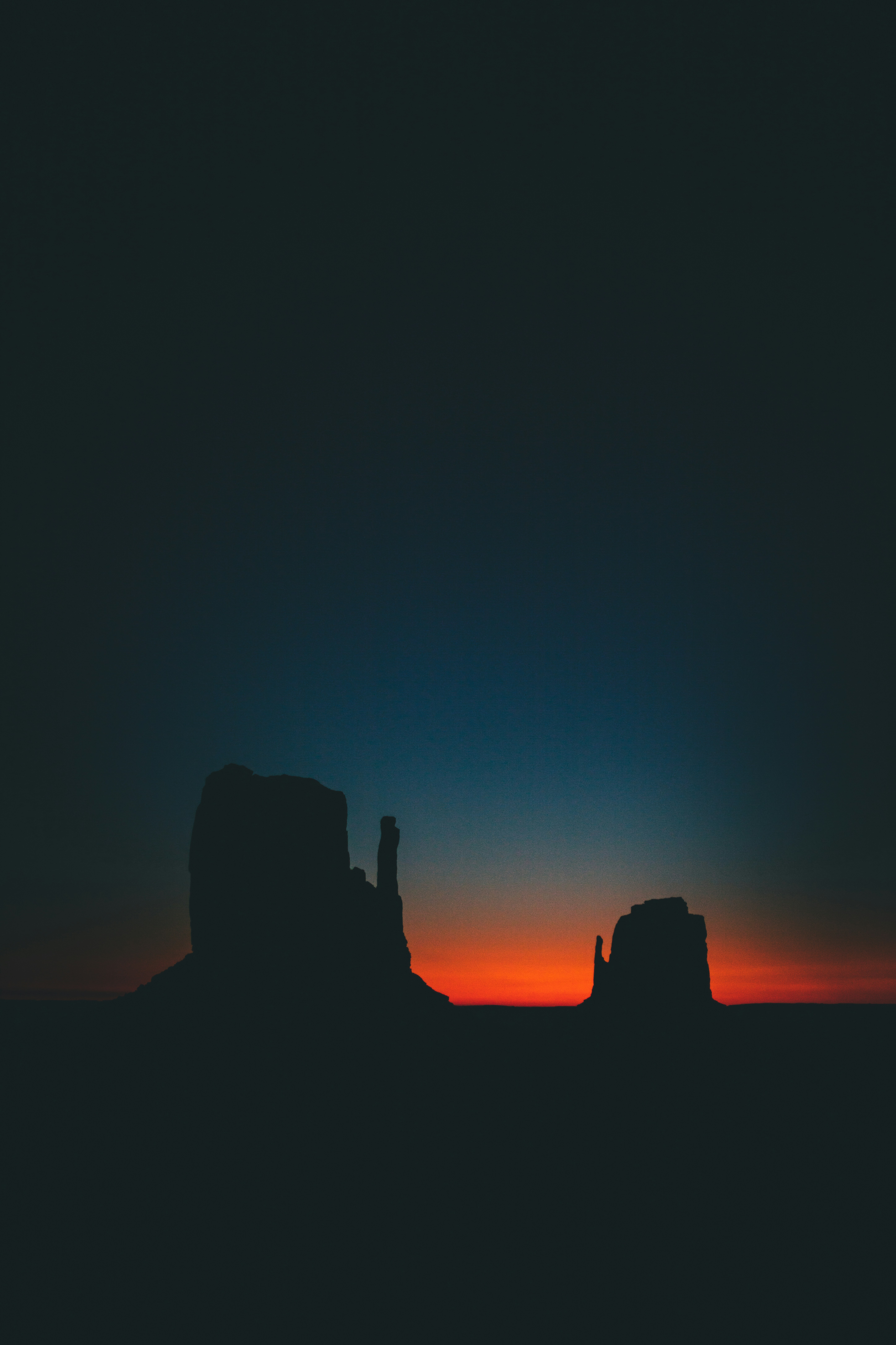 Silhouetted rock formations against a vibrant twilight sky transitioning from deep blue to fiery orange. Perfectly captures the serene beauty of the desert landscape.