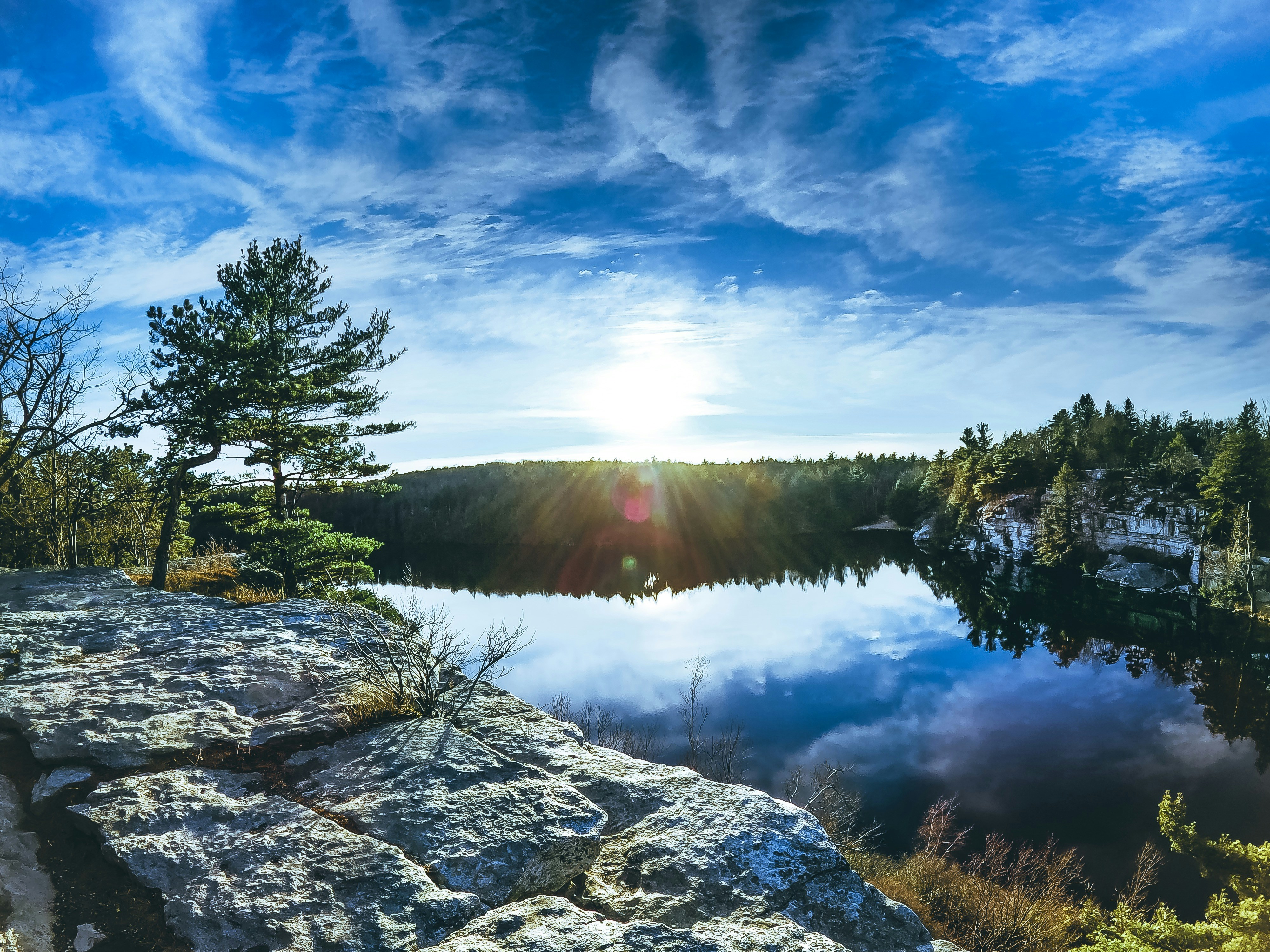 Rocky cliff overlooking a tranquil lake under a bright sunlit sky.