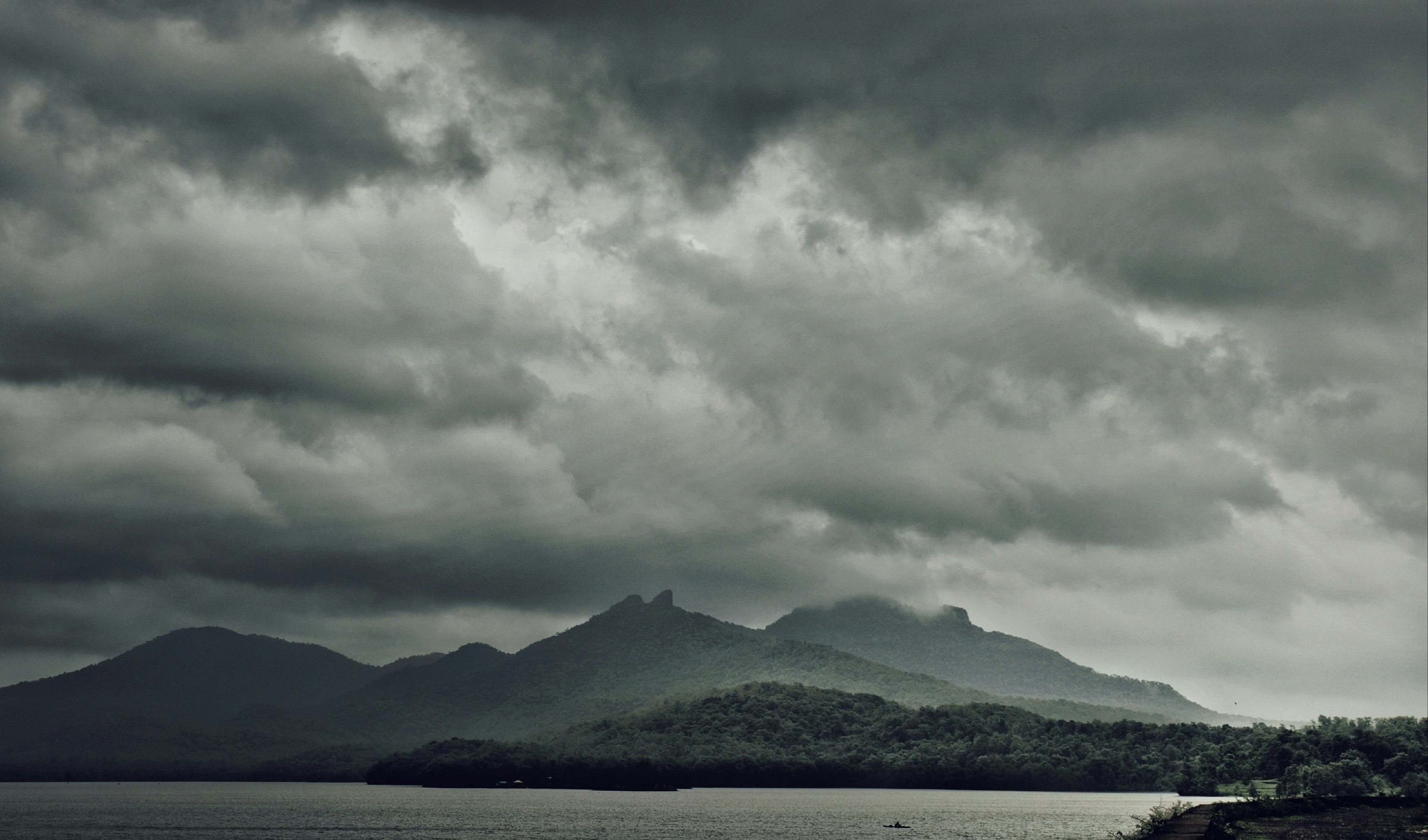Dramatic clouds loom over a serene lake with distant mountains on the horizon.