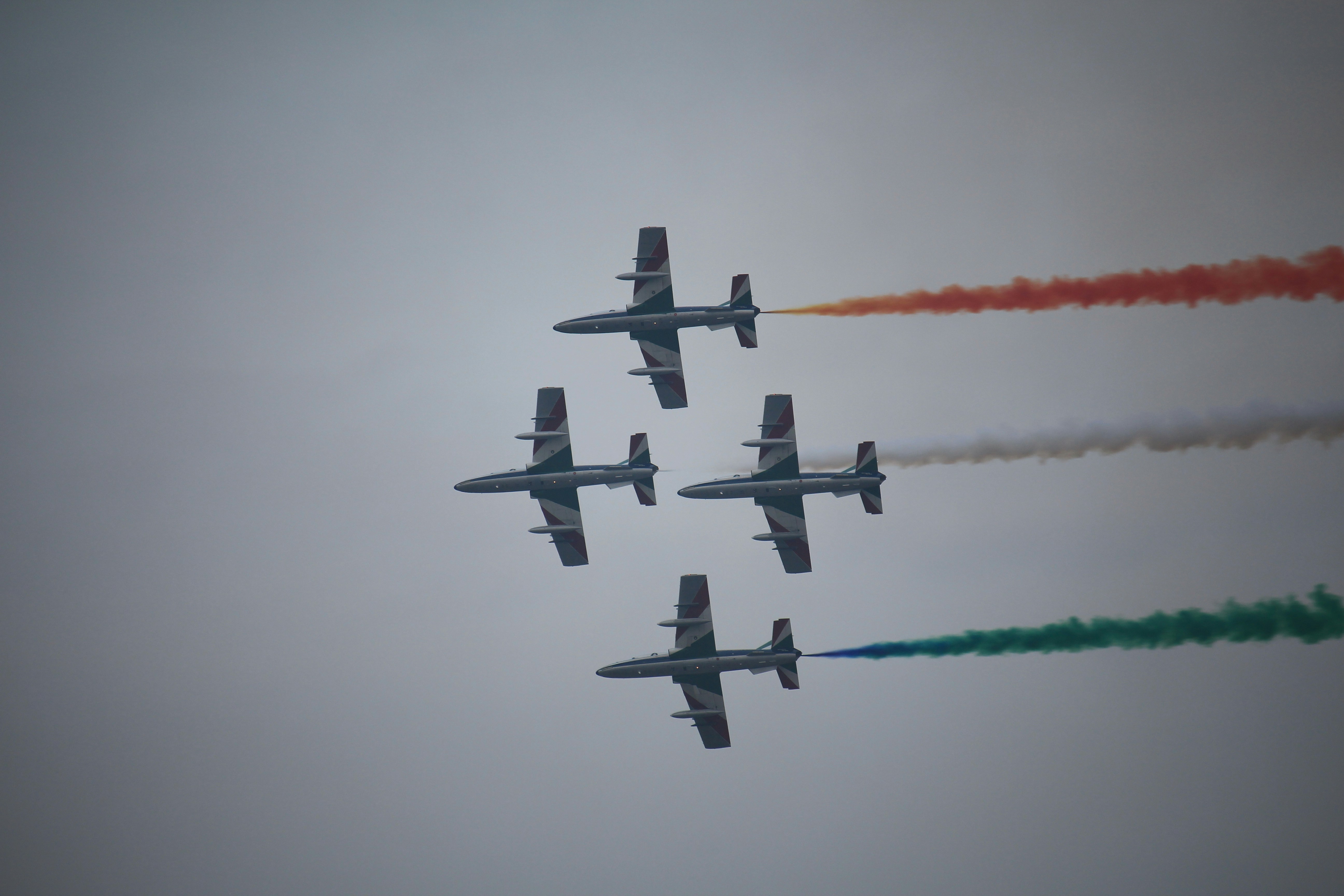 Four agile aircraft race in close formation leaving colored contrails under a muted sky.
