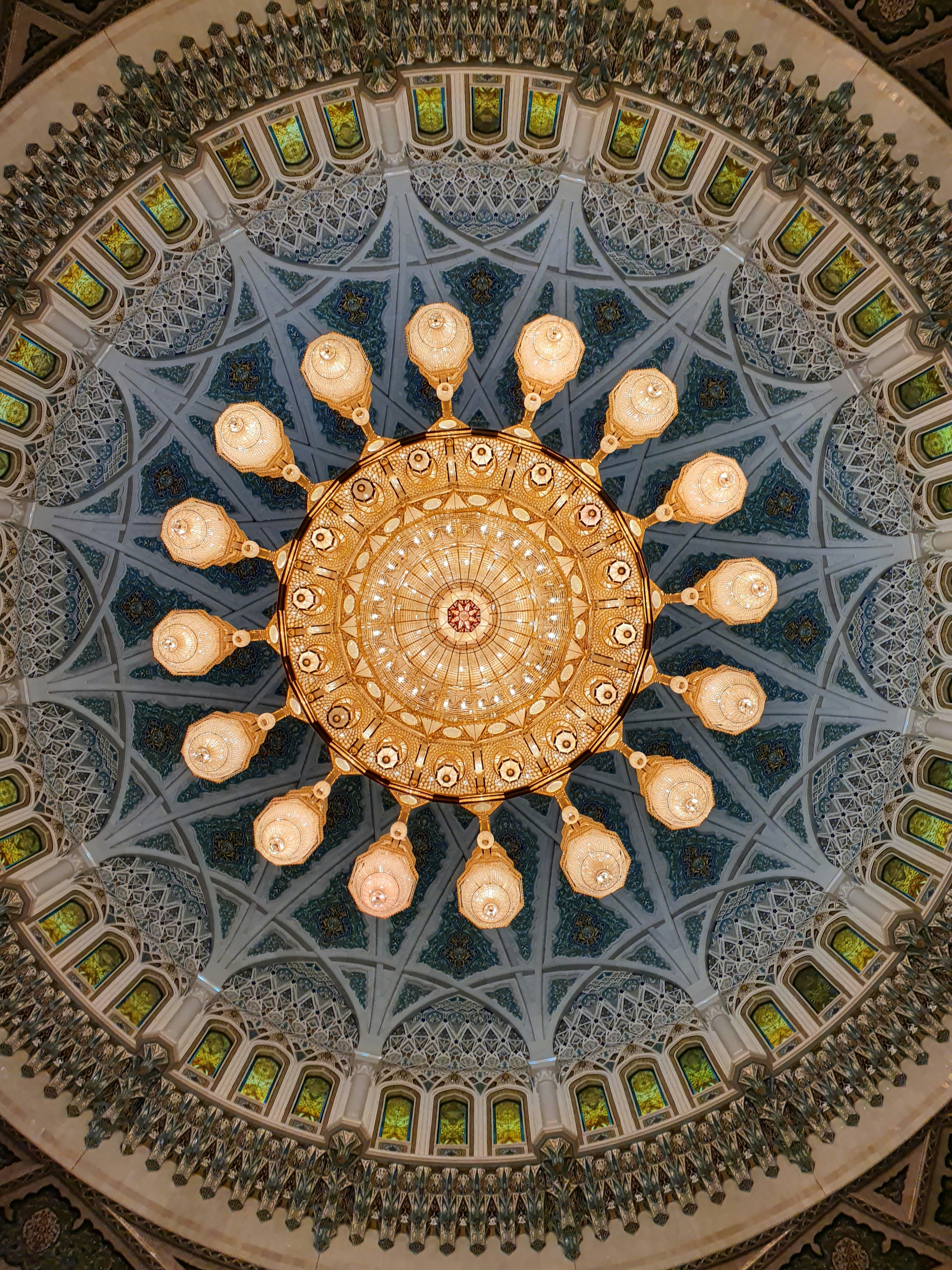 Intricately designed chandelier suspended from a beautifully patterned dome, showcasing ornate details and vibrant colors.