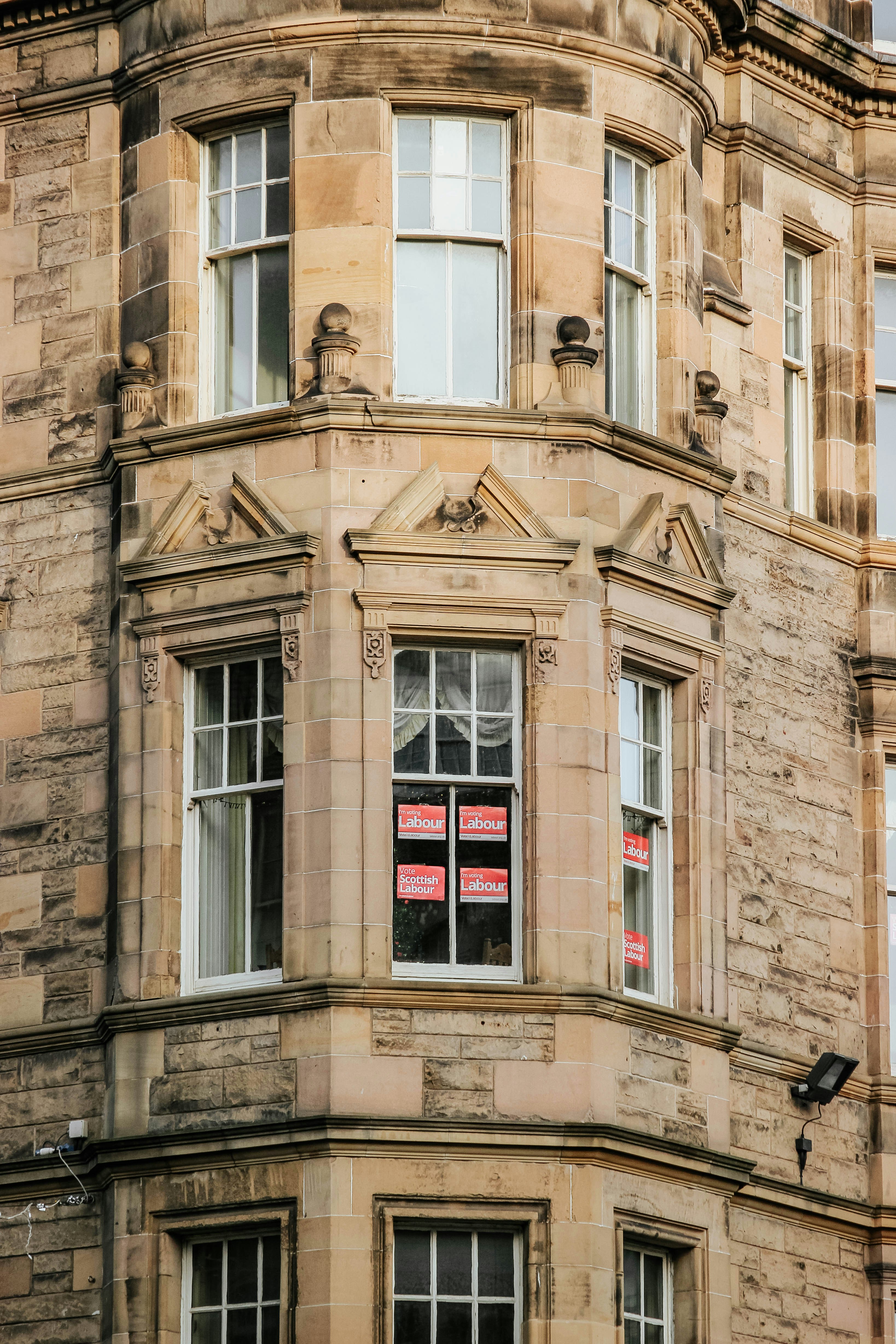 Victorian-style building showcasing ornate stonework and large windows, featuring prominent Labour campaign posters in the foreground.
