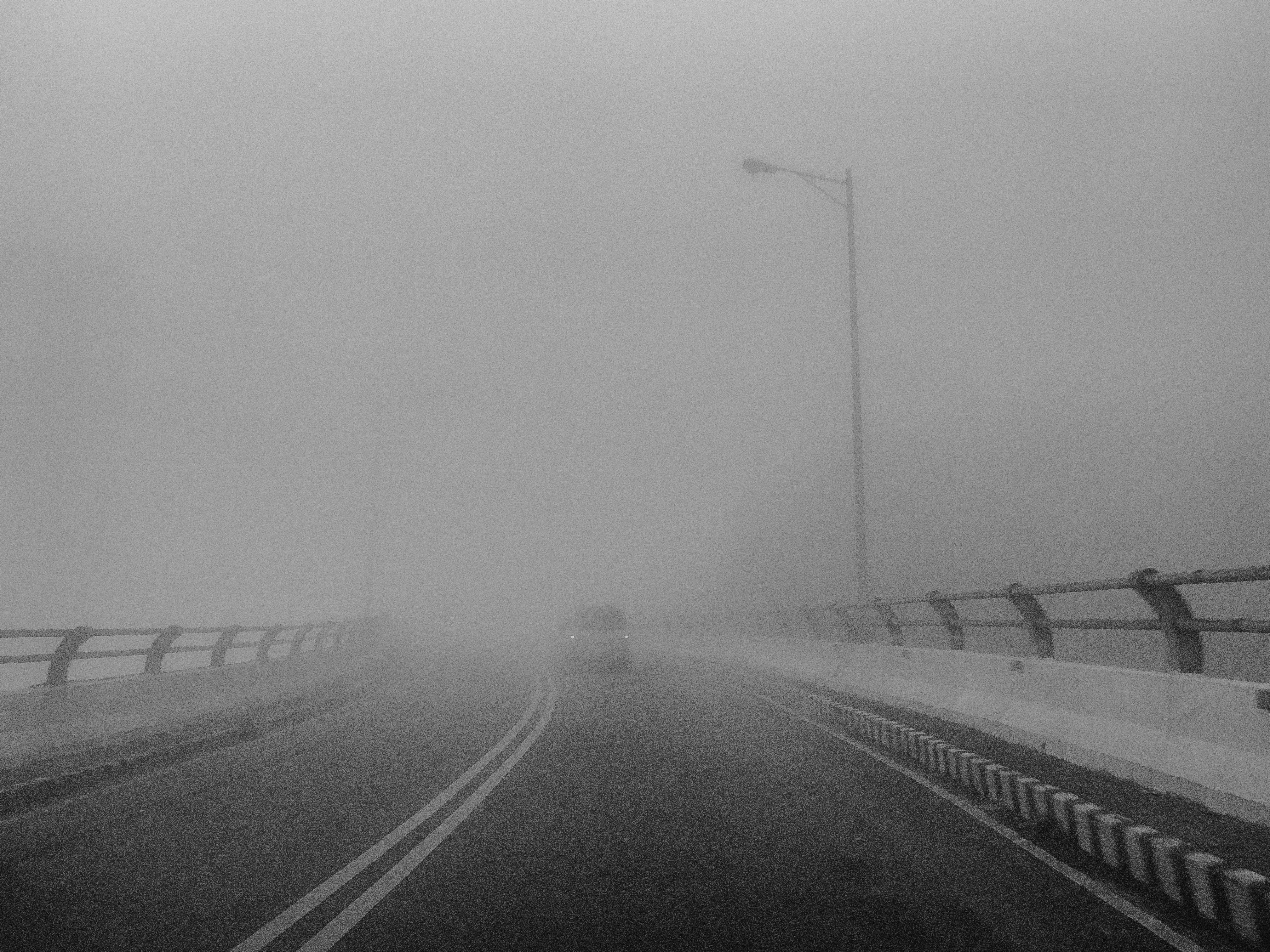 Car driving on a fog-covered bridge with limited visibility.