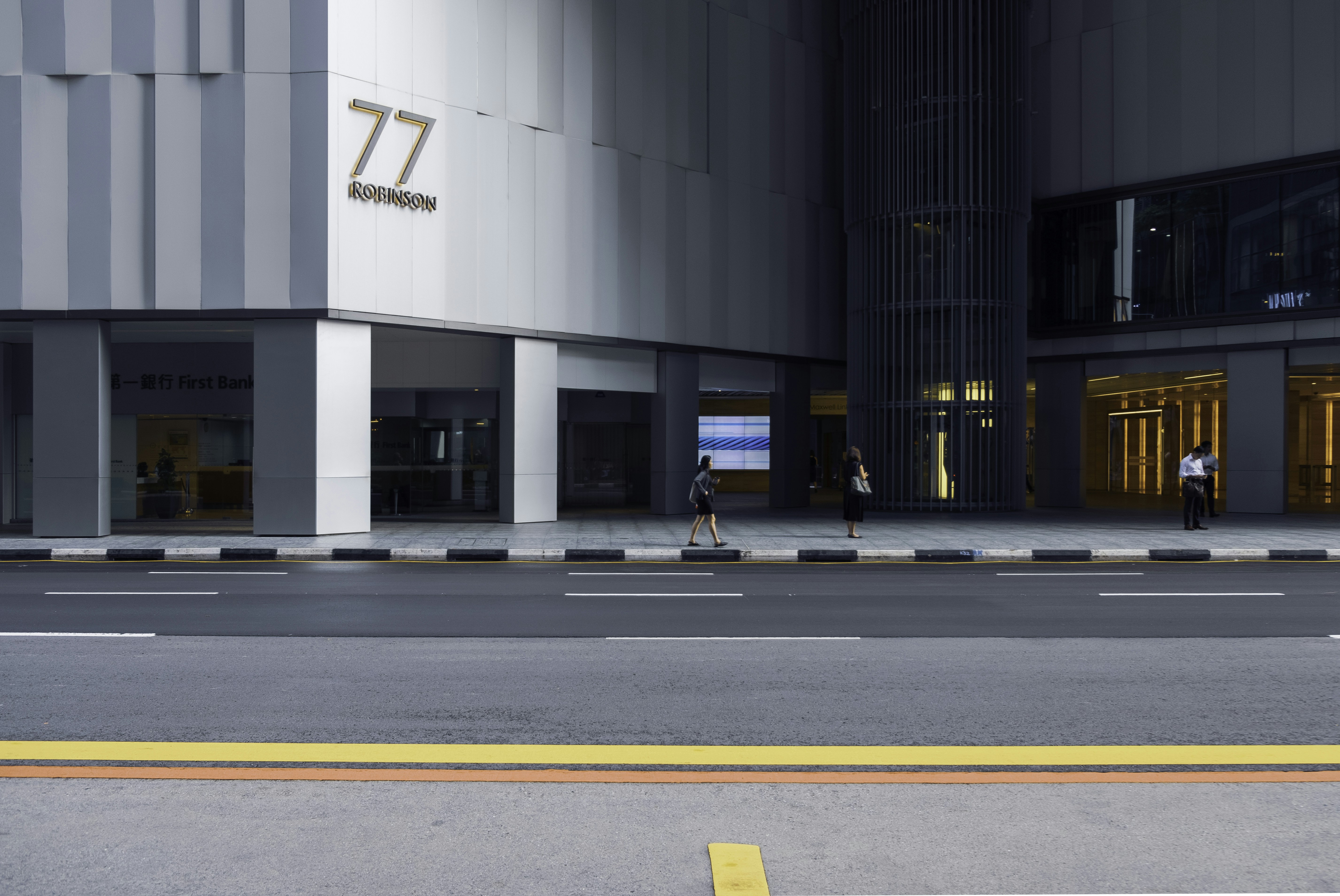 Pedestrians walk past the modern facade of 77 Robinson Road, featuring sleek lines and reflective surfaces.