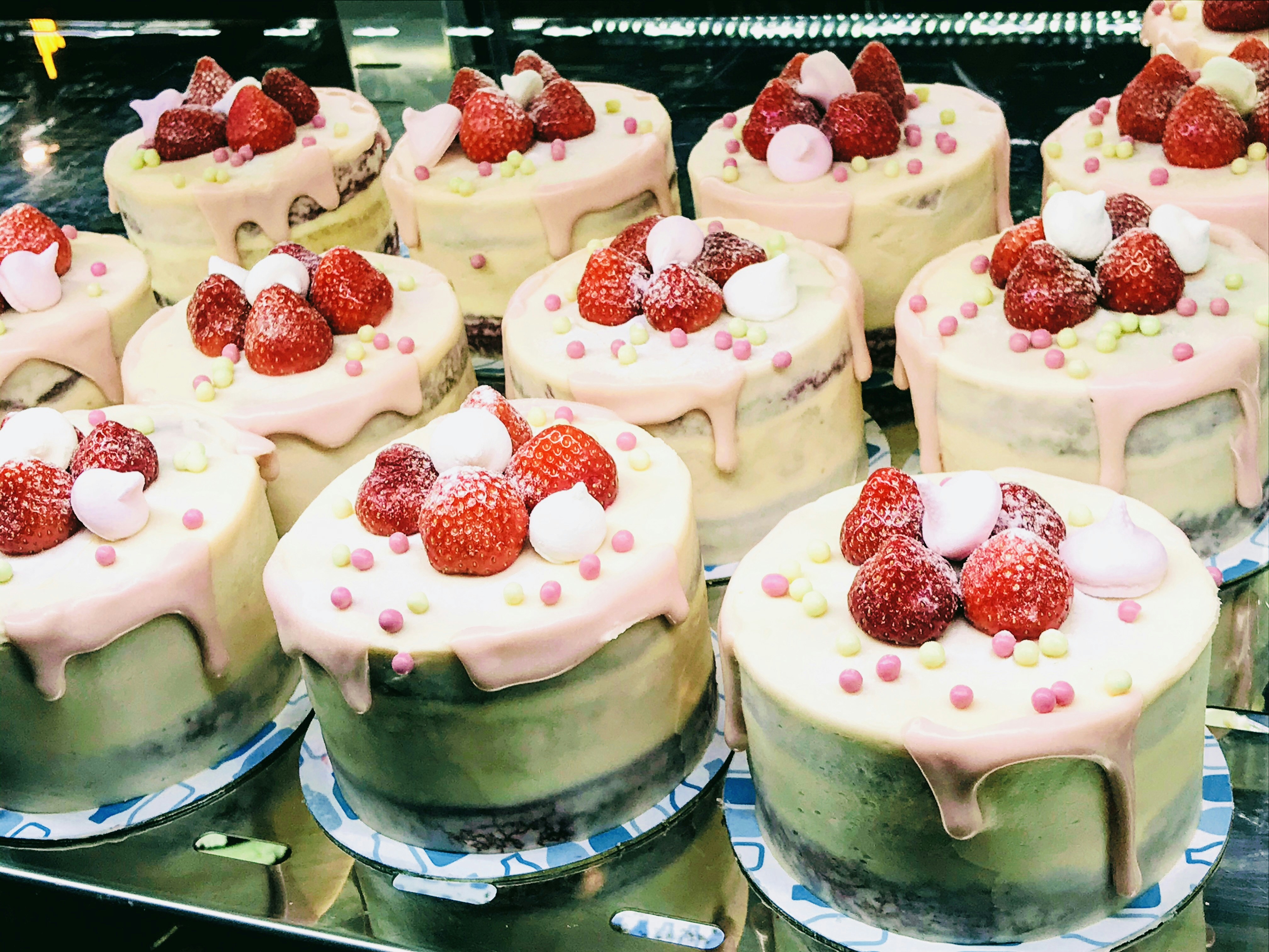 Pastel Cakes in a Display Case: Pink Drips and Strawberry Crowns