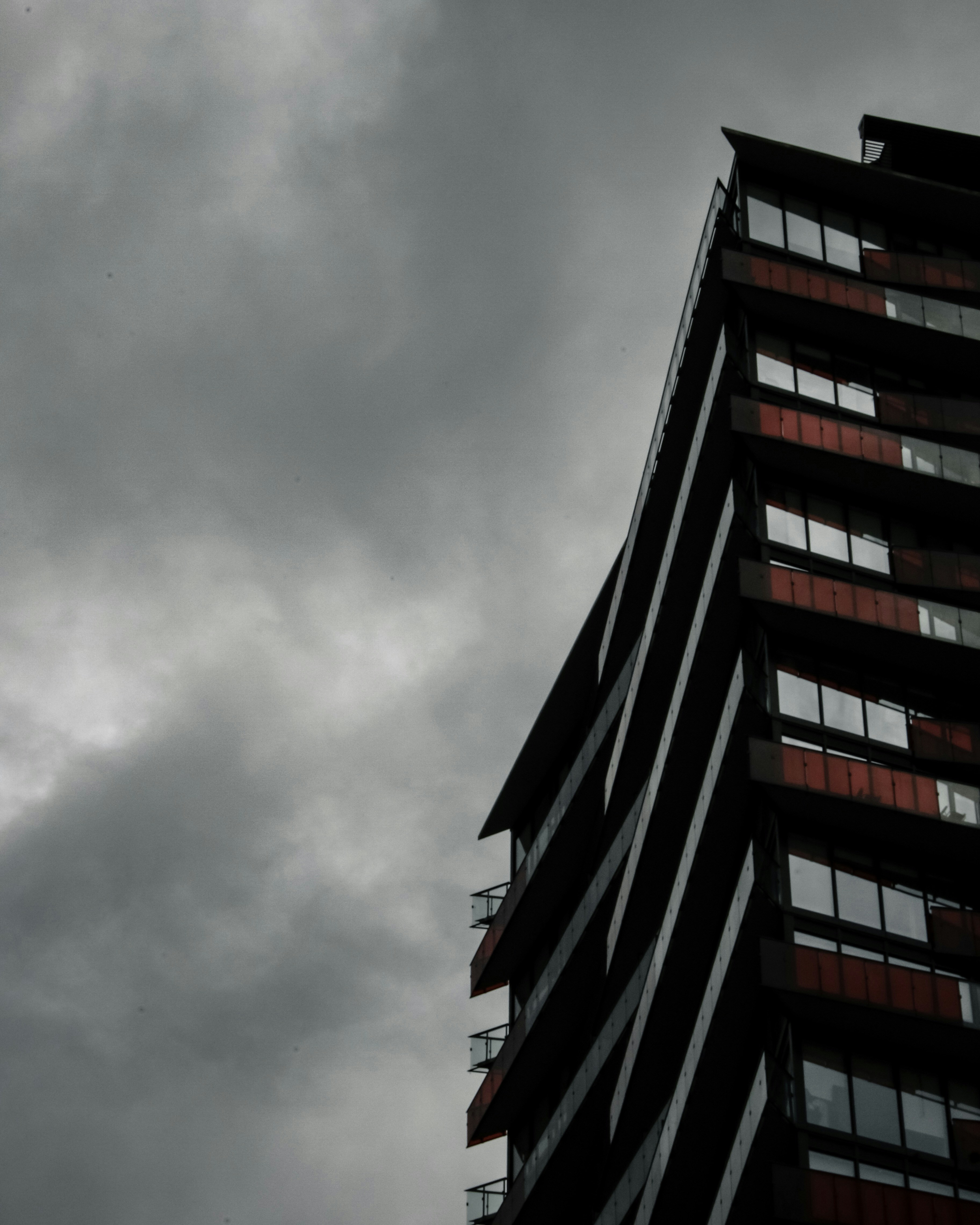 Angular building facade with dark glass and red accents, set against a backdrop of ominous clouds.