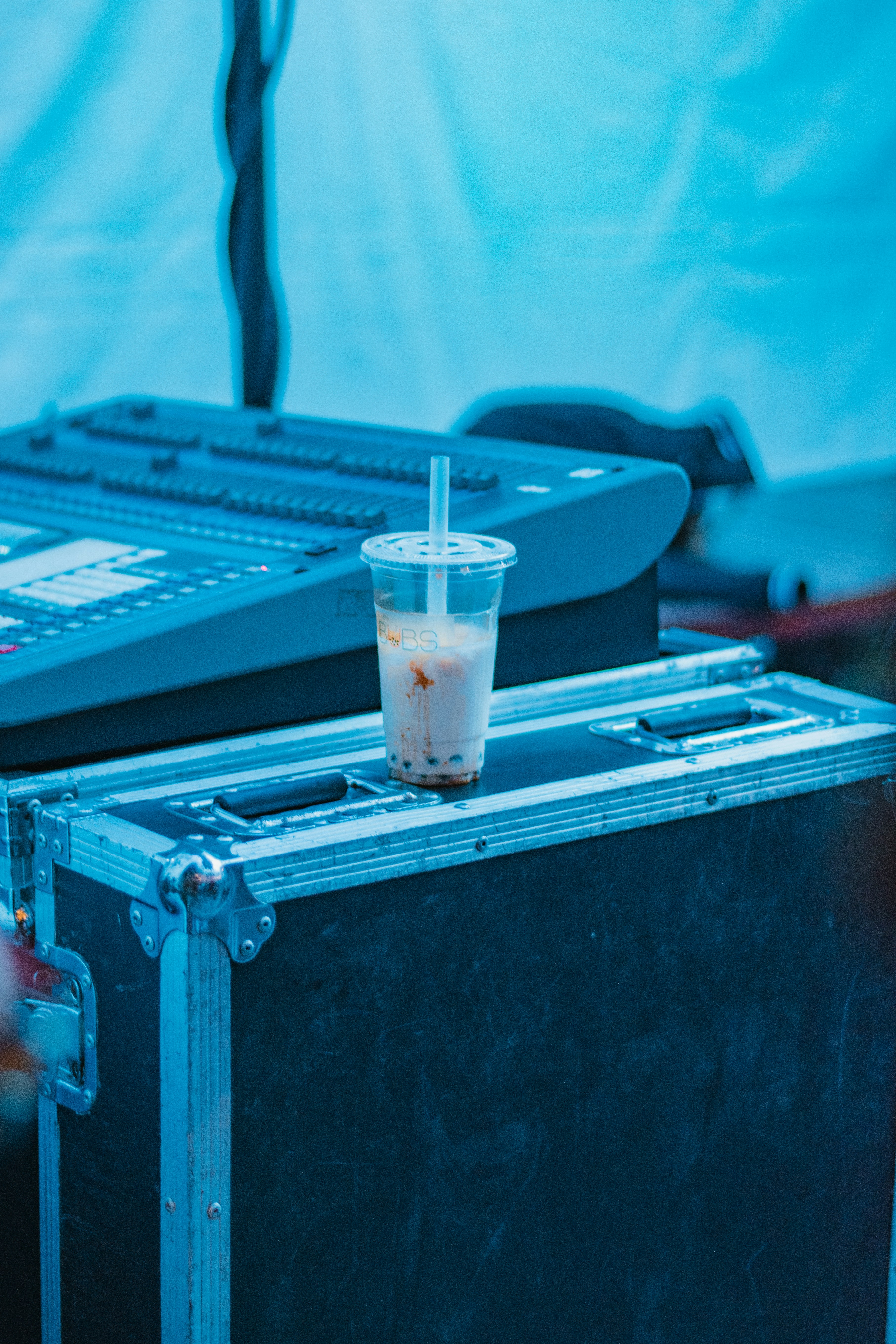 Iced coffee resting on a soundboard case at an event, surrounded by a cool blue ambiance.