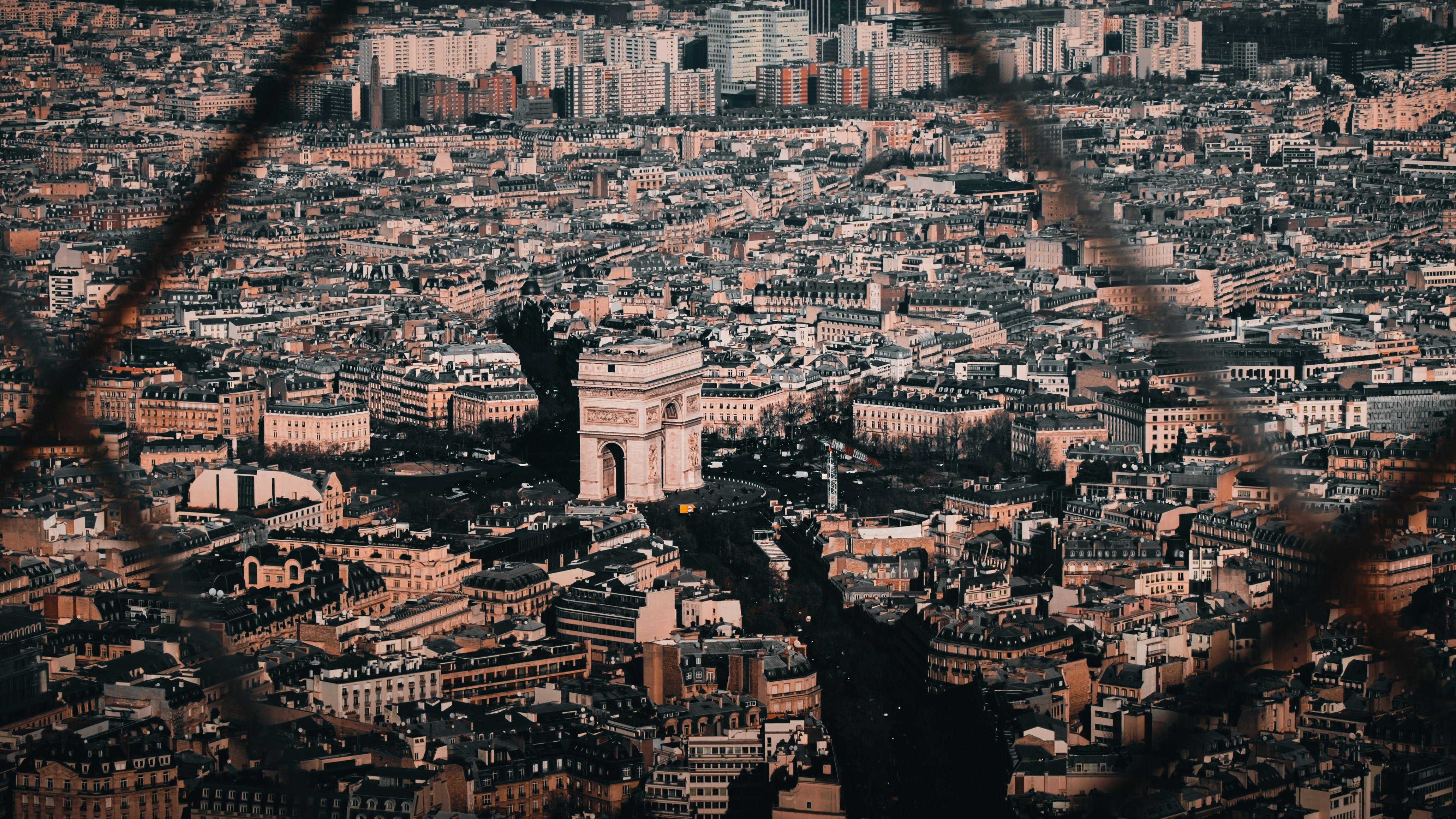 Aerial view of Paris showcasing the Arc de Triomphe surrounded by the city's intricate layout, framed by a geometric pattern.