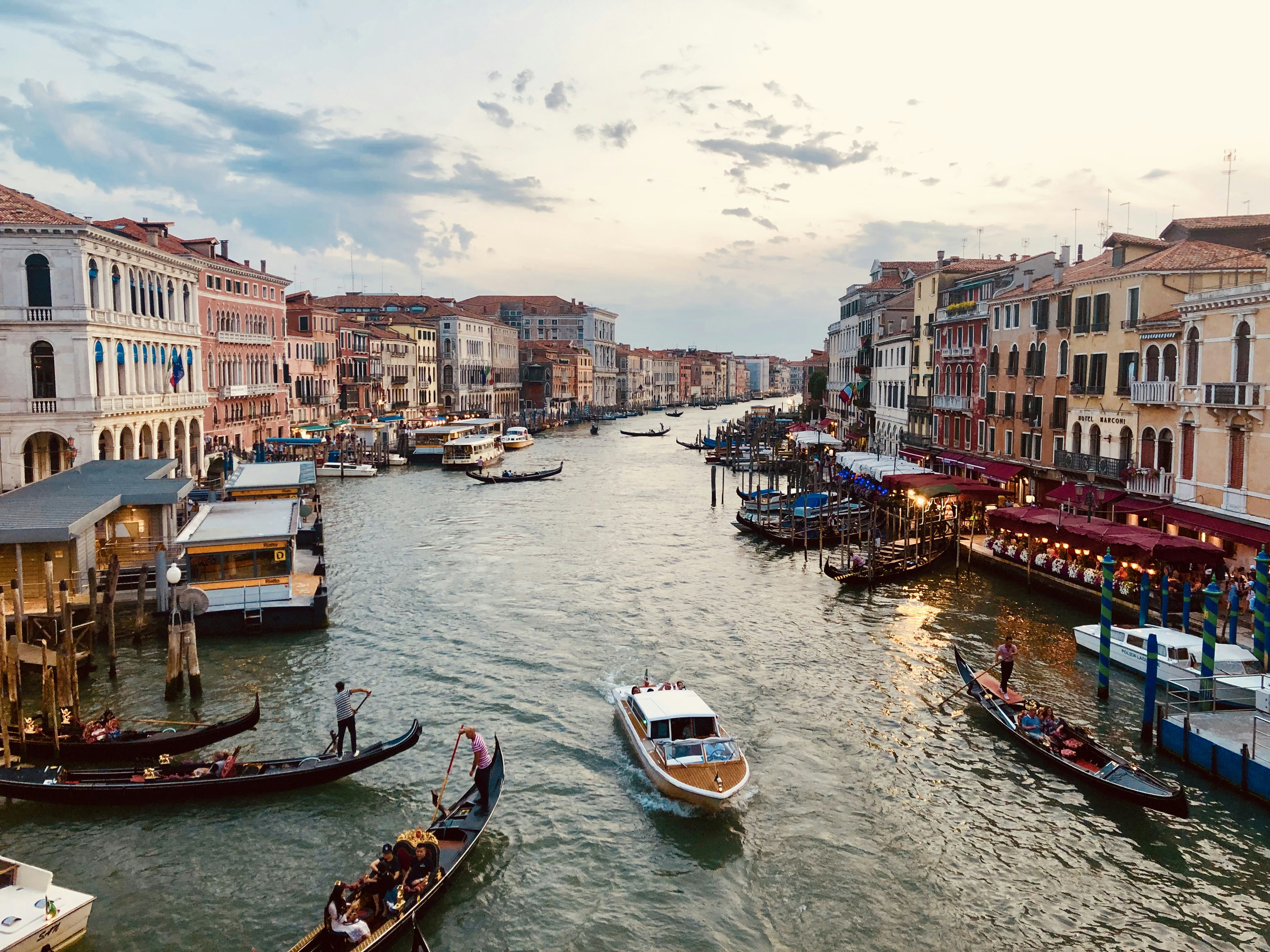 Boats and gondolas navigate a bustling canal flanked by historic buildings at dusk.
