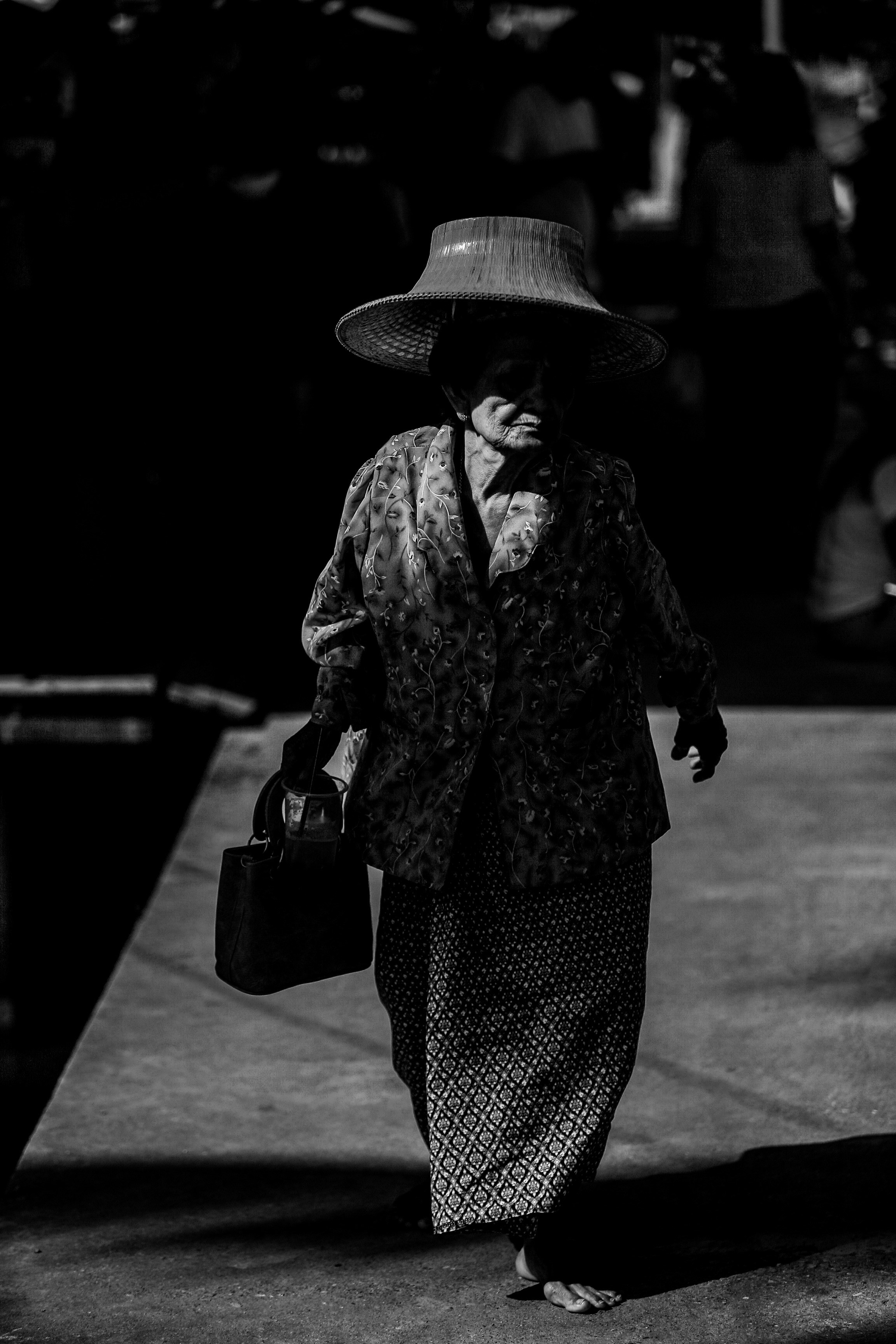 Hatted Quiet: An Elder Woman Traverses a Shadowed Street