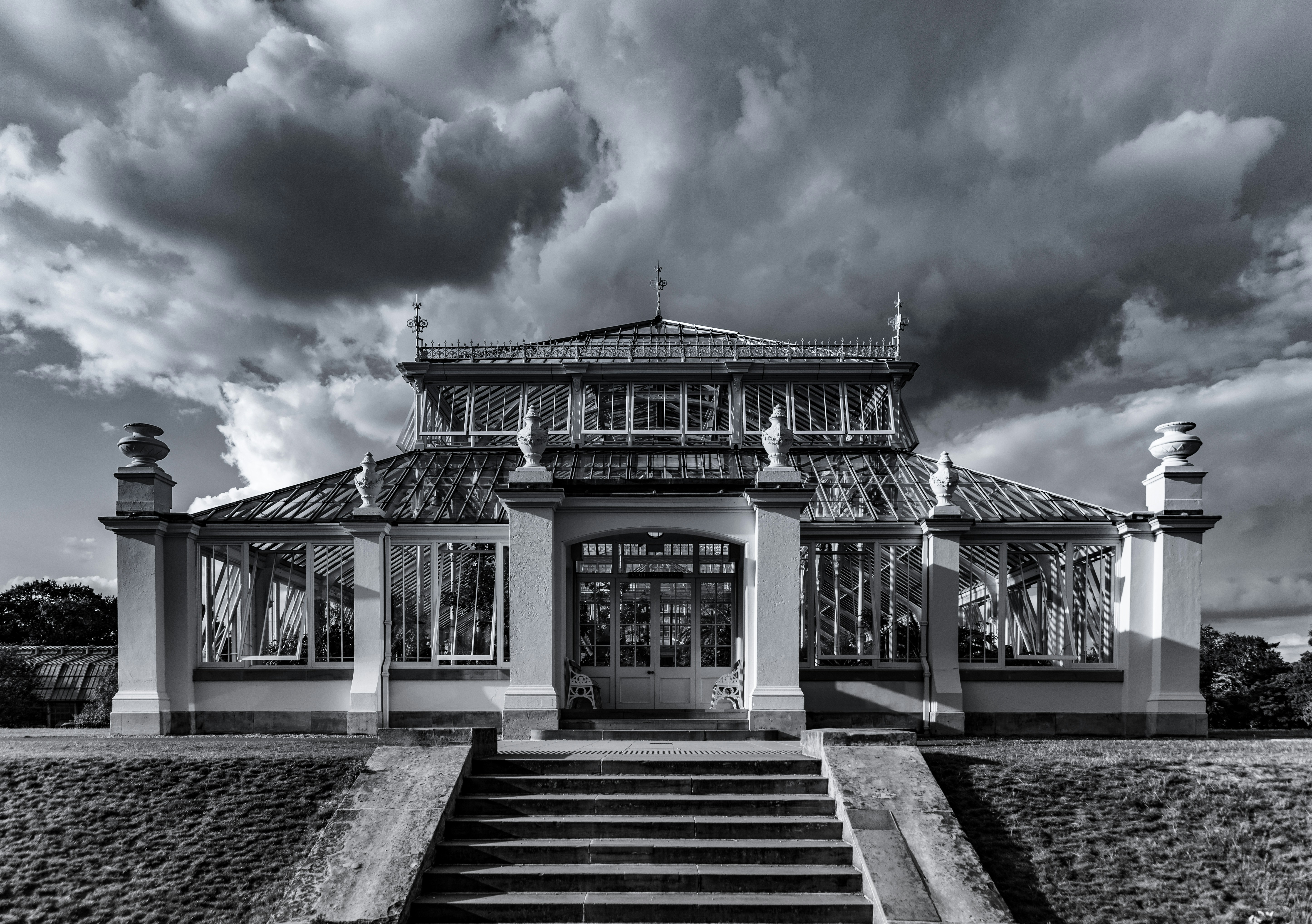 Ornate glasshouse with intricate architecture set against dramatic cloud formations.