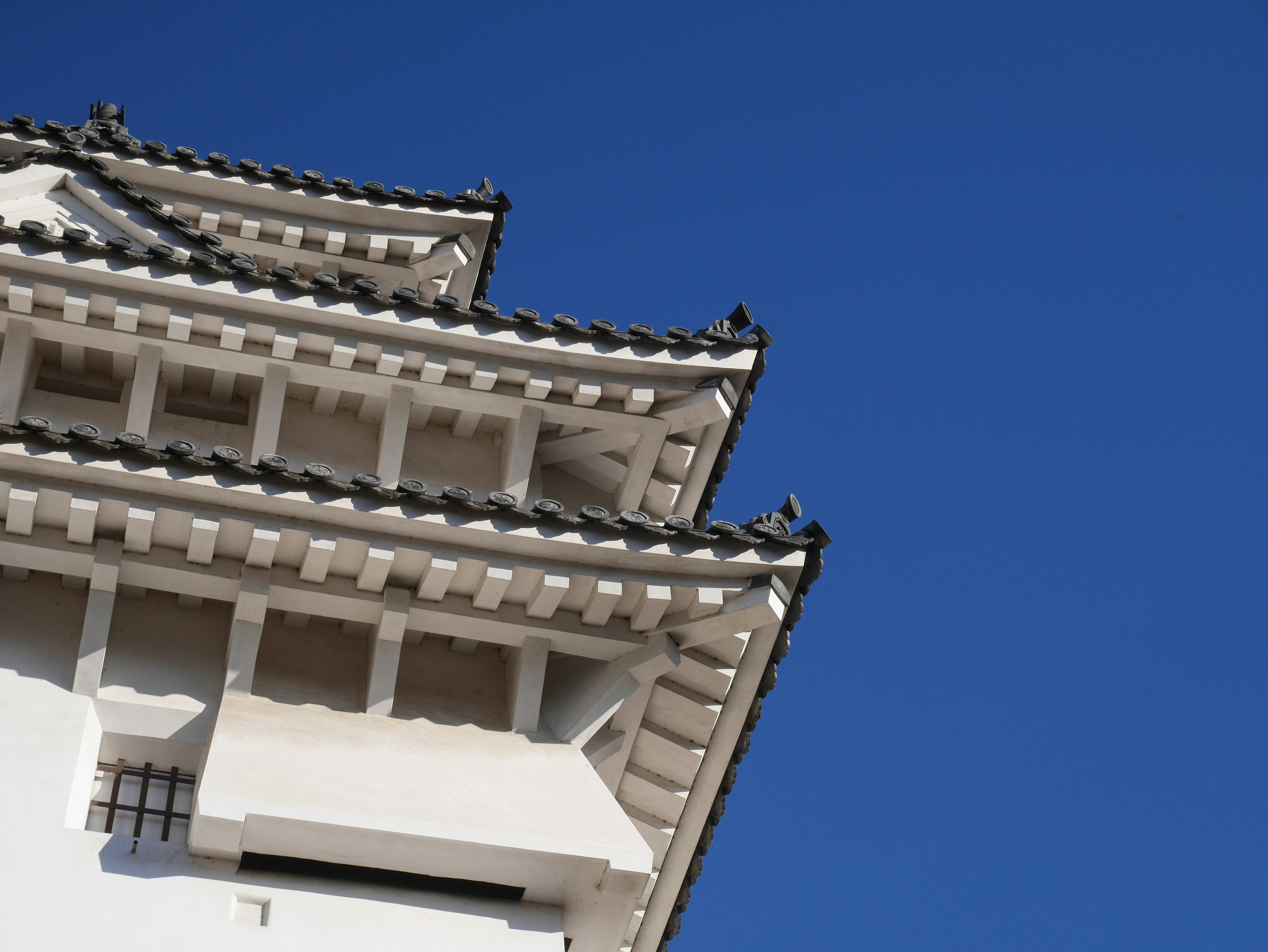 White and black pagoda roof with intricate details set against a clear blue sky.