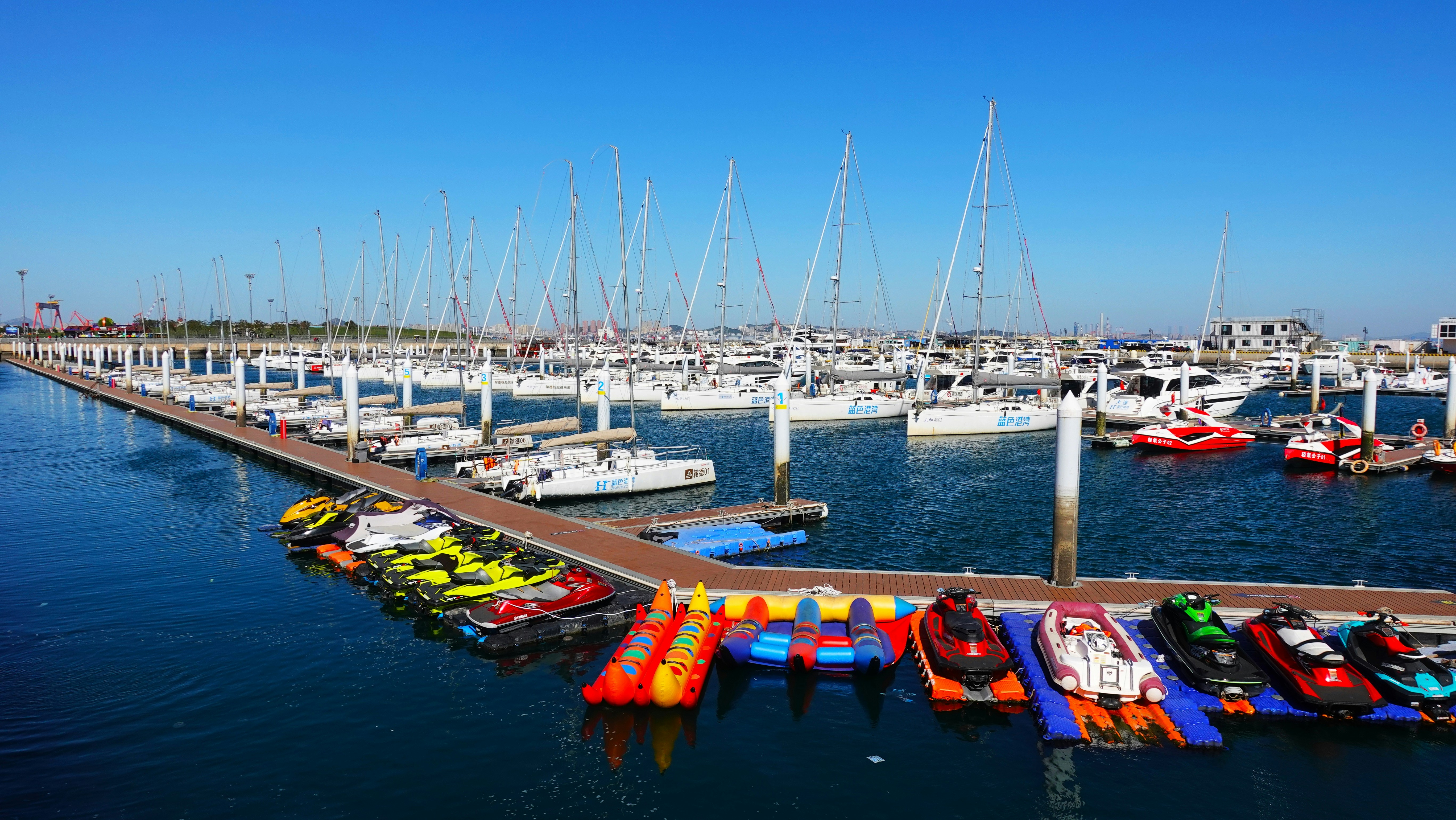 Colorful kayaks line the dock at a bustling marina under a clear blue sky.