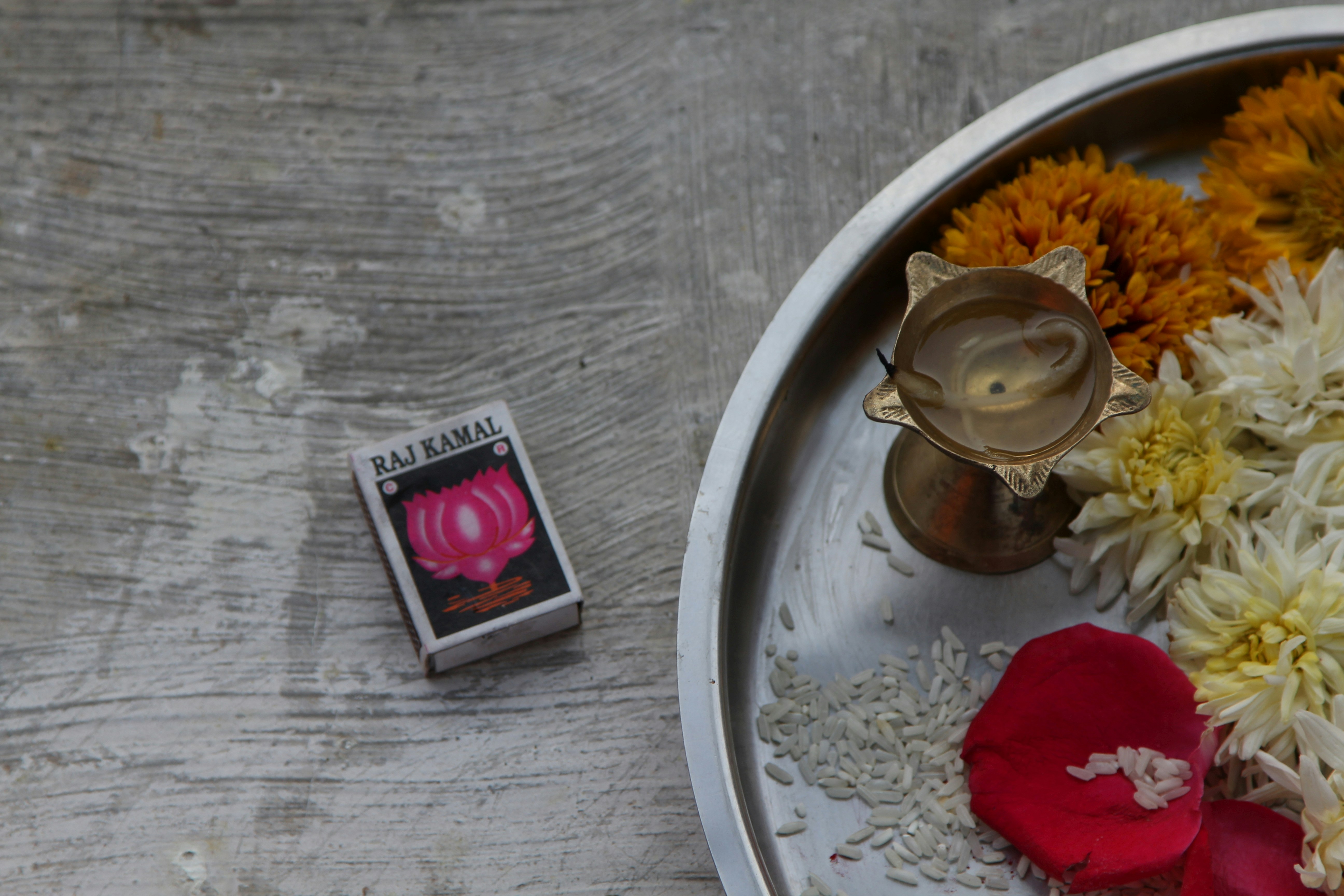 Red and white Raj Kamal matchbox beside a tray of flowers and rice ...