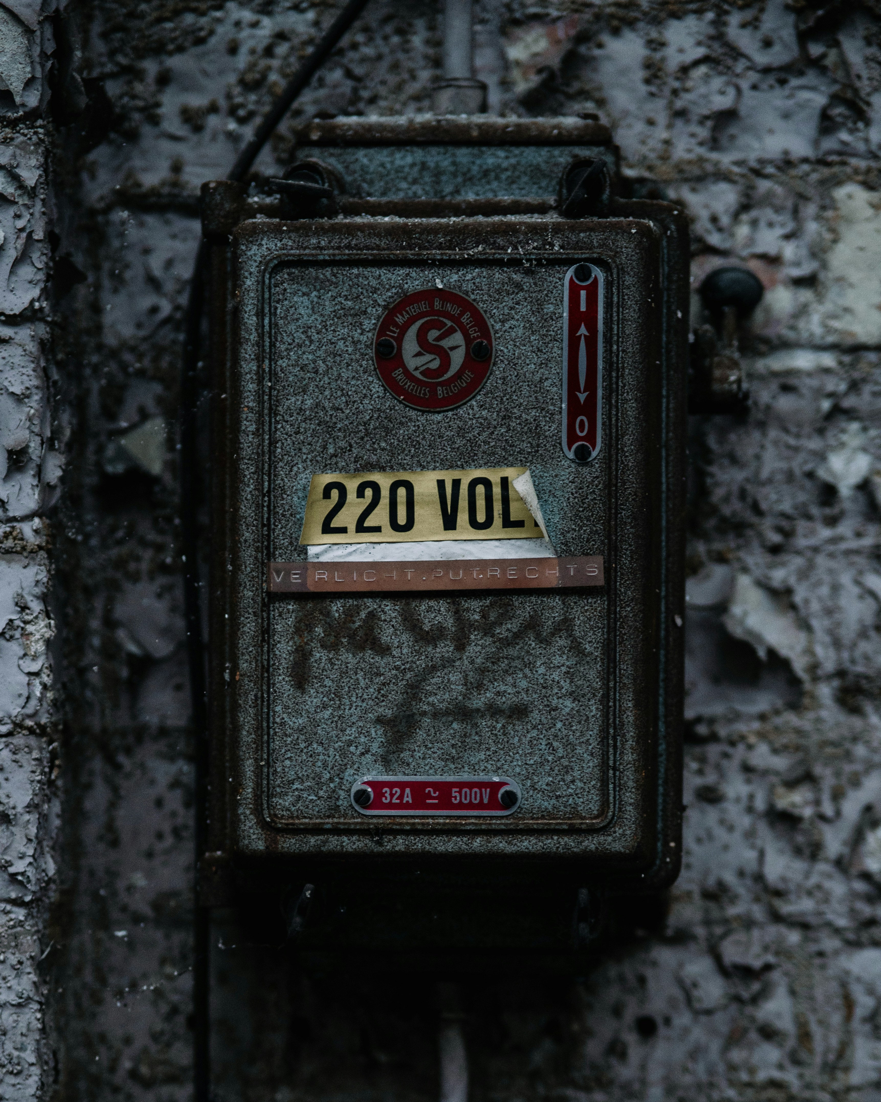 Weathered electrical box mounted on a peeling wall, showcasing a faded label reading '220 VOL.'