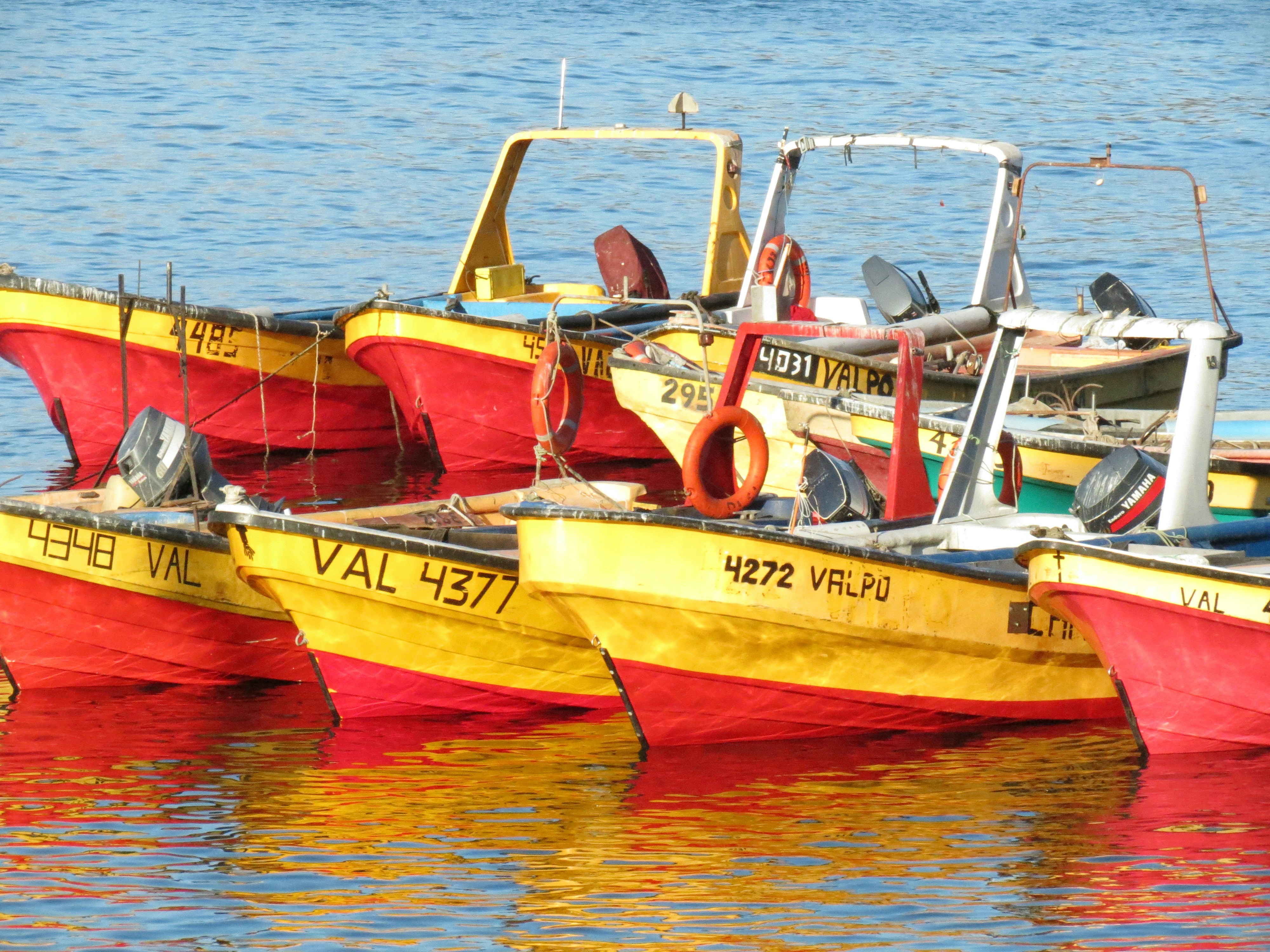 Brightly colored boats with yellow and red hulls moored on calm blue water.
