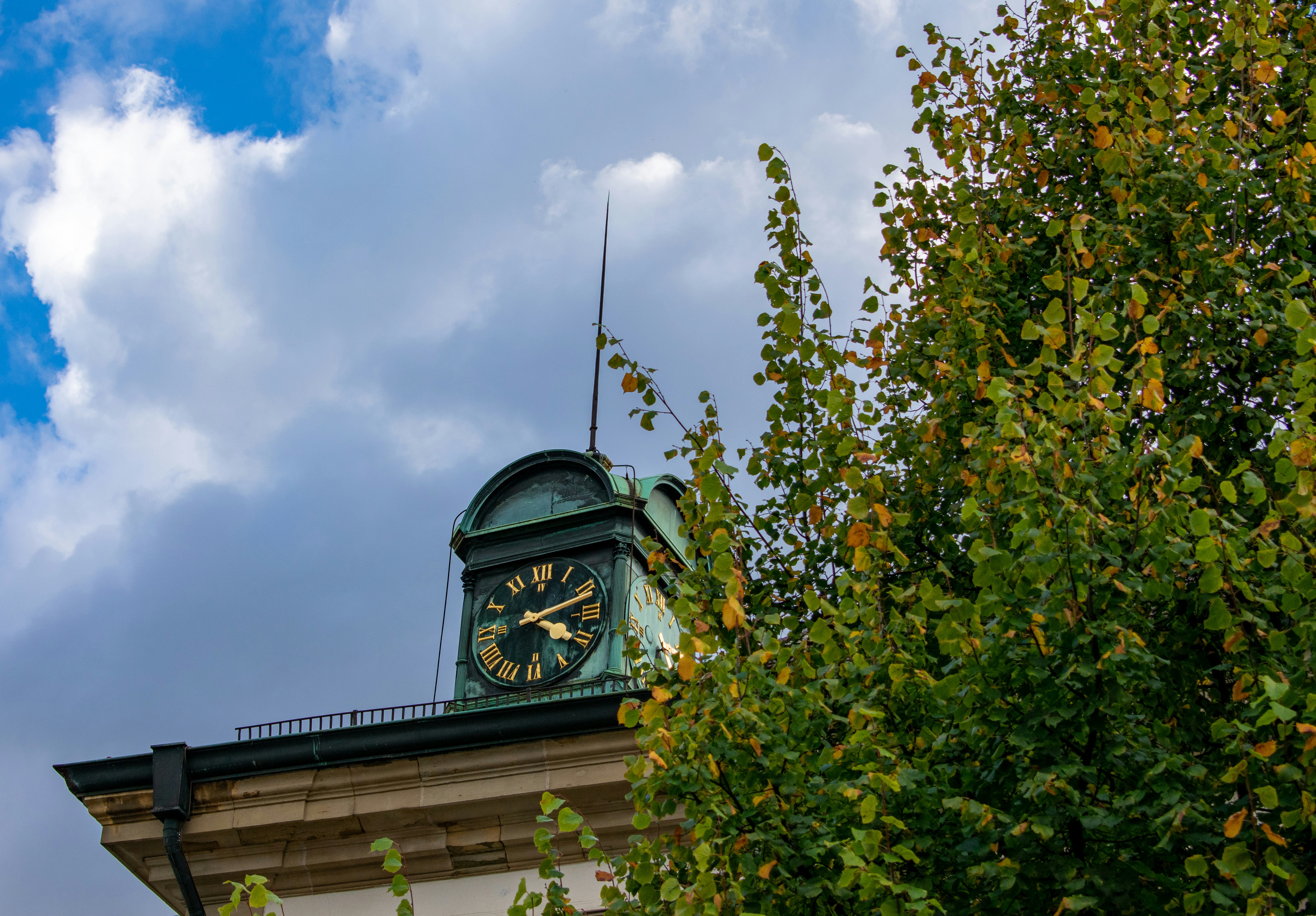 Clock tower peeks through vibrant autumn foliage against a backdrop of blue sky and clouds.