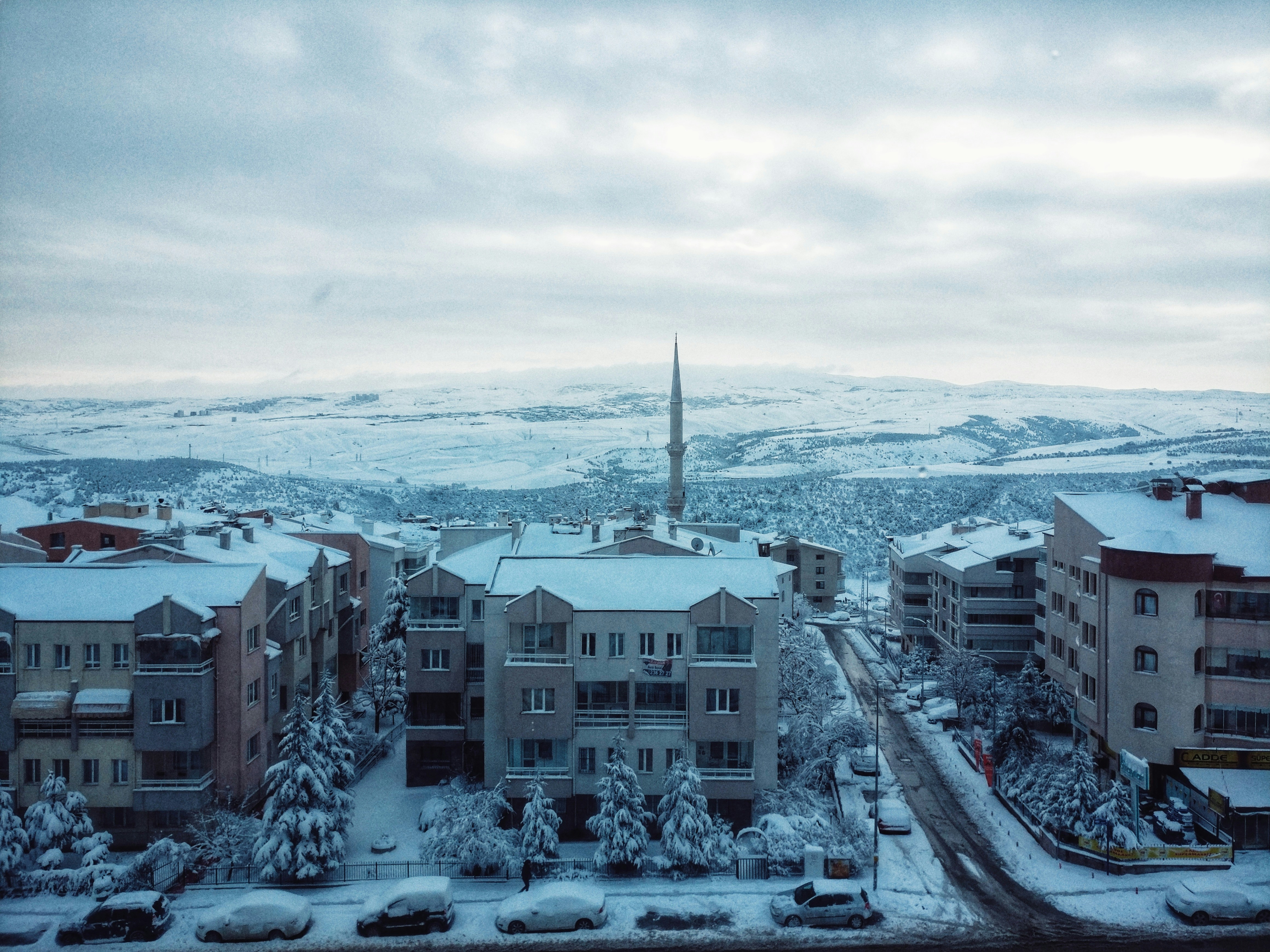 Snow-covered neighborhood with a distant mosque under a cloudy sky.