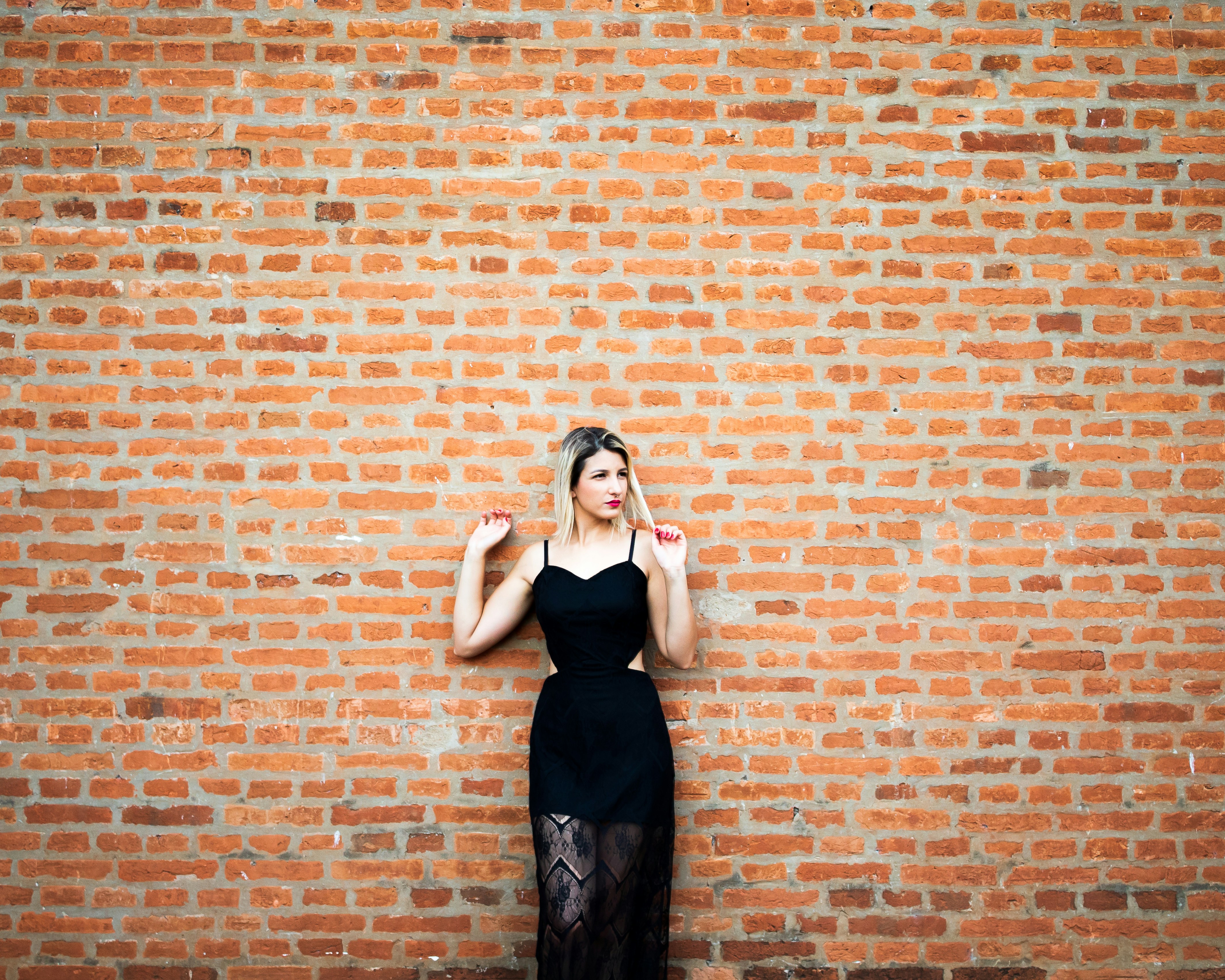 Woman in a black dress poses against a red brick wall.