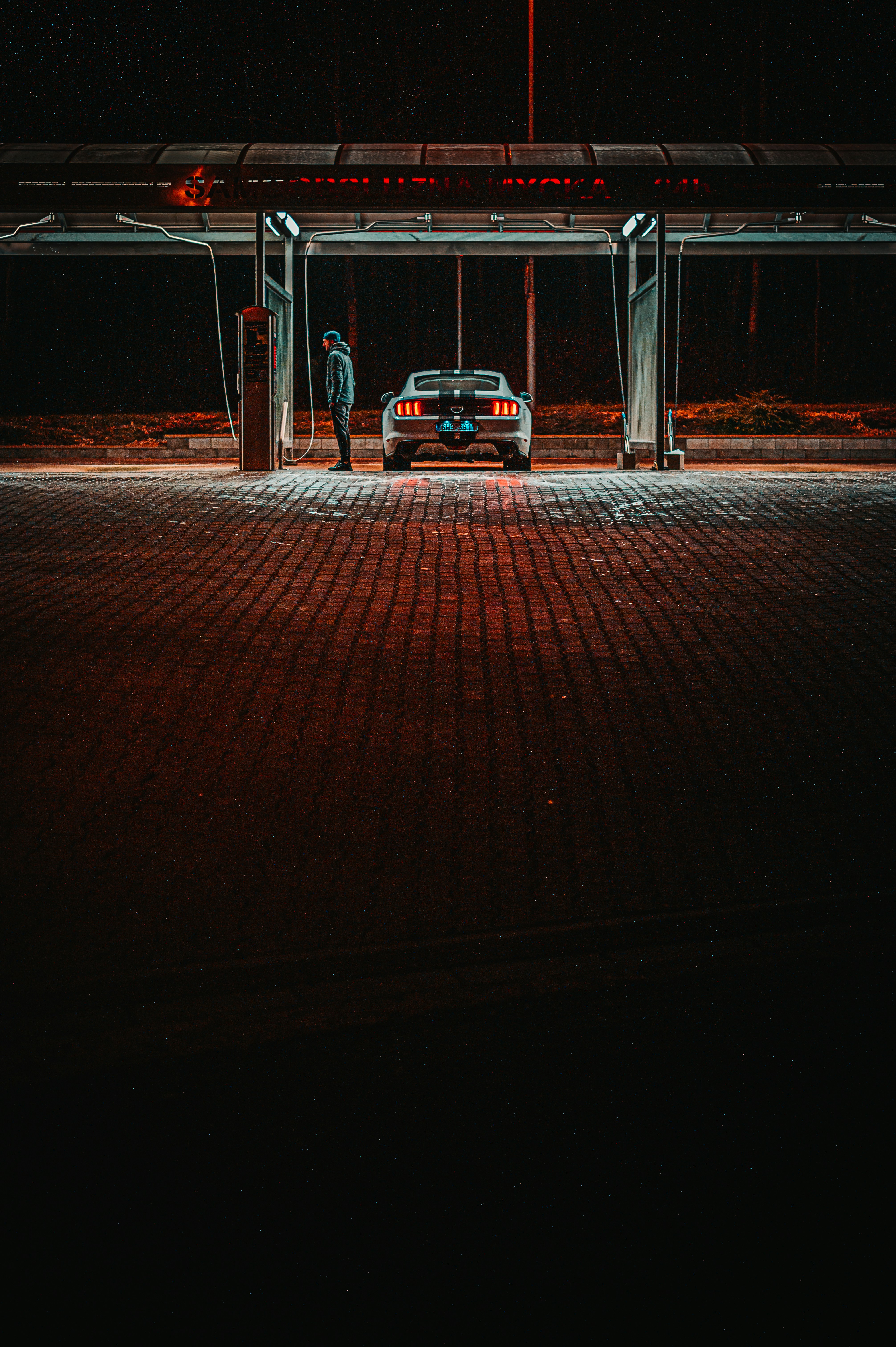 A lone figure stands by a sleek electric vehicle at a dimly lit charging station, surrounded by a serene nighttime atmosphere.