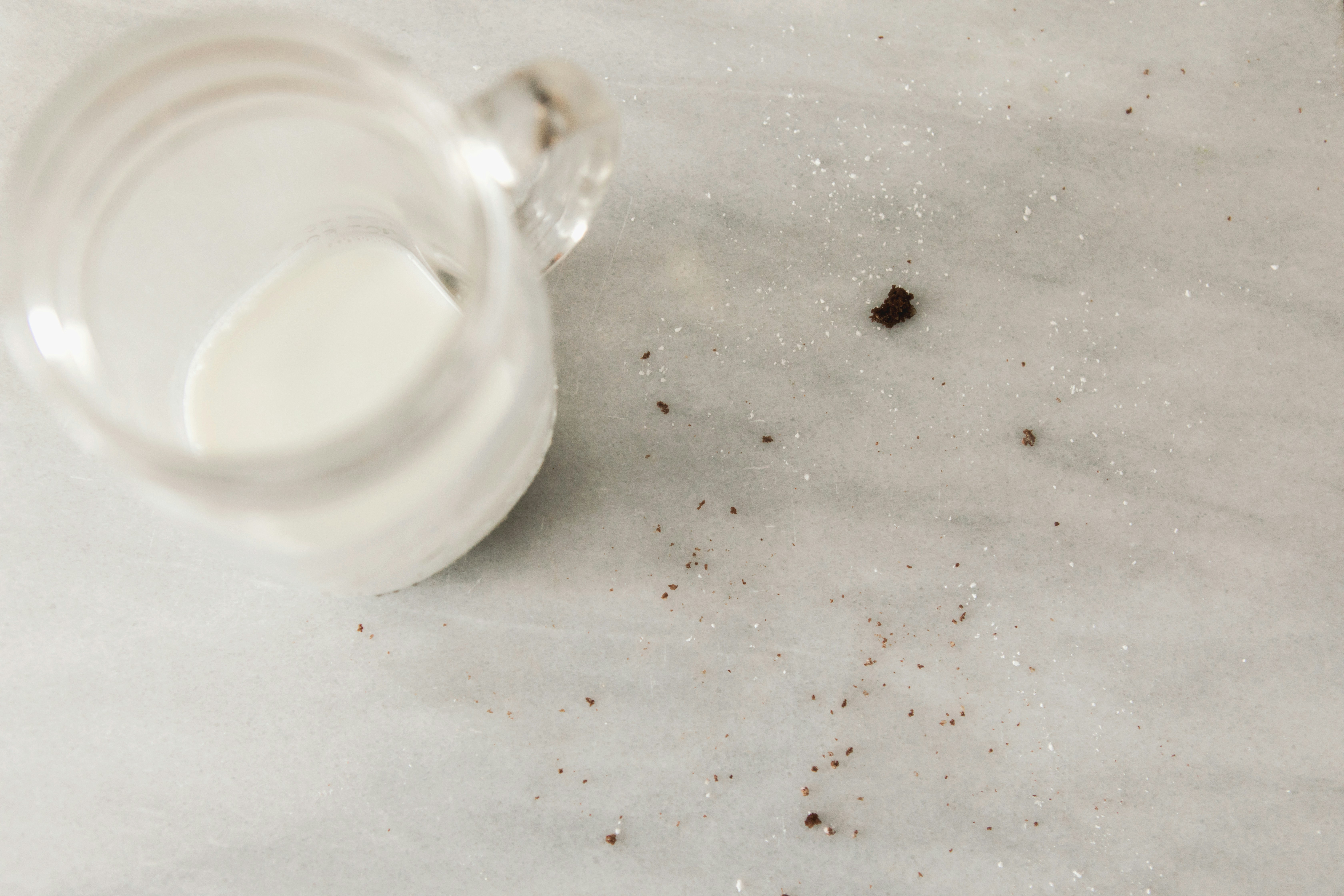 A glass jar filled with milk sits on a marble surface, surrounded by scattered coffee grounds, hinting at a recent brewing ritual.