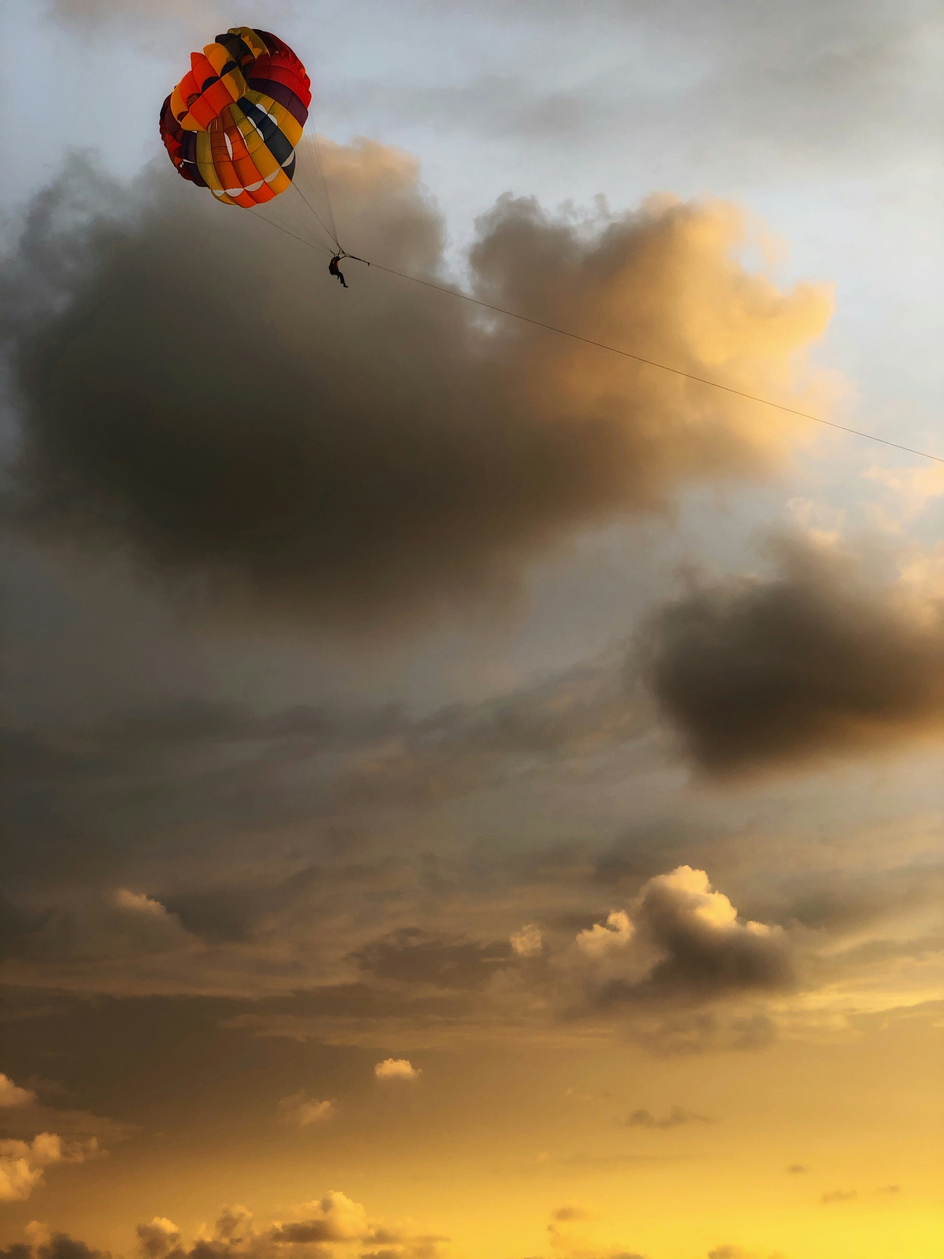 A colorful parachute glides gracefully against a backdrop of dramatic clouds and a golden sky during sunset.