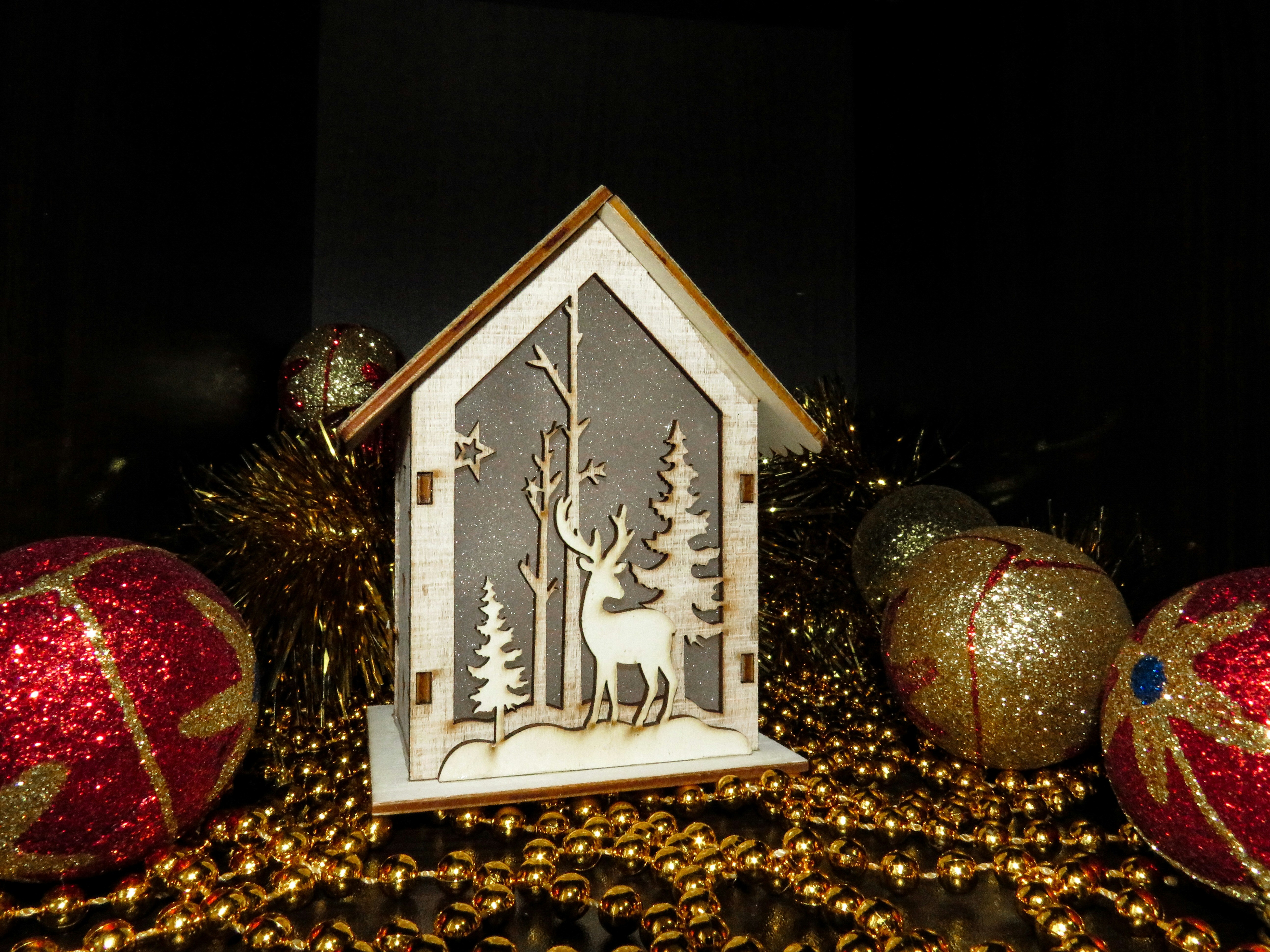 Wooden winter-scene ornament featuring a deer among trees, set among gold beads and glittering Christmas balls.