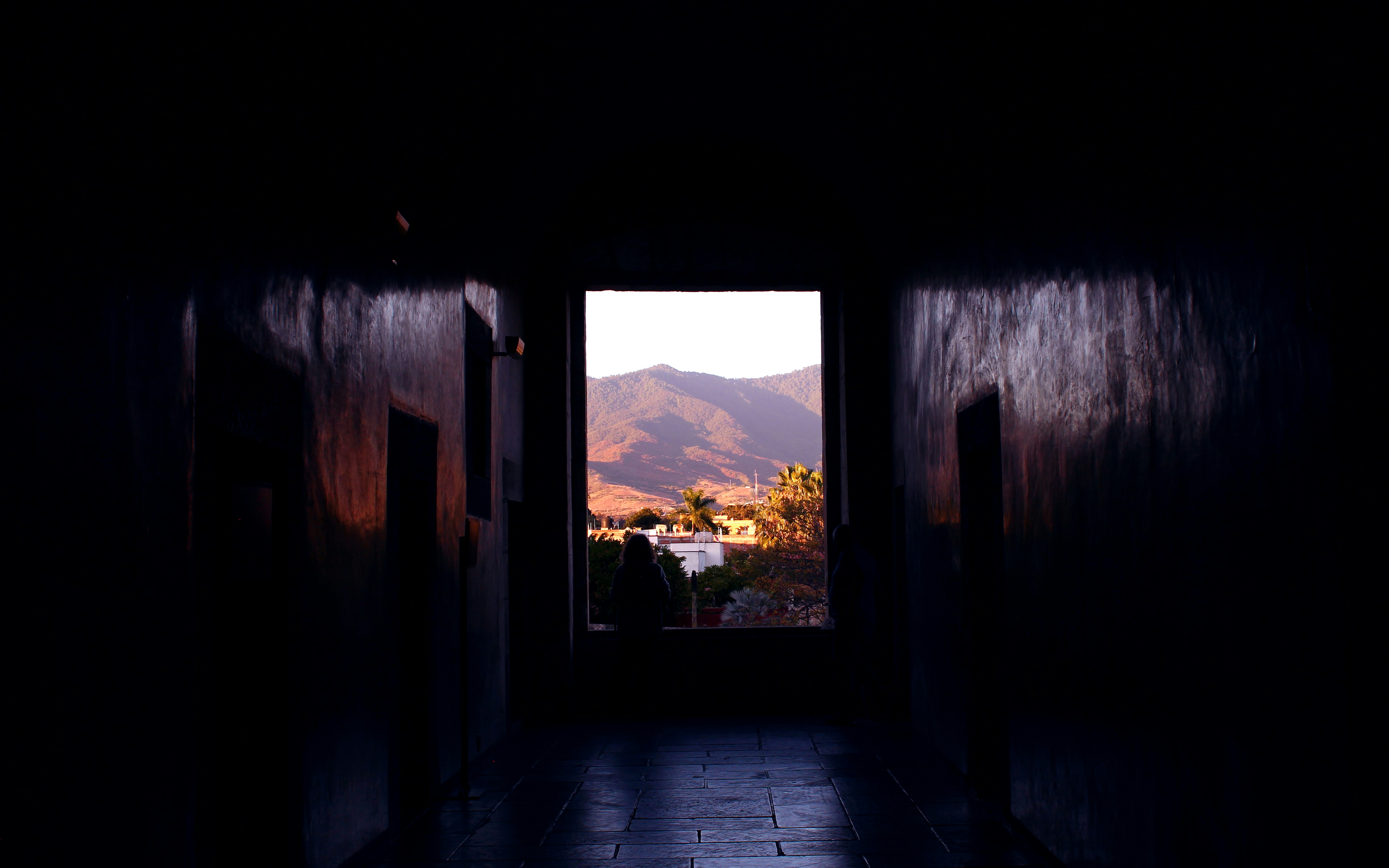 Distant mountains glow at sunset through a dark corridor's window.