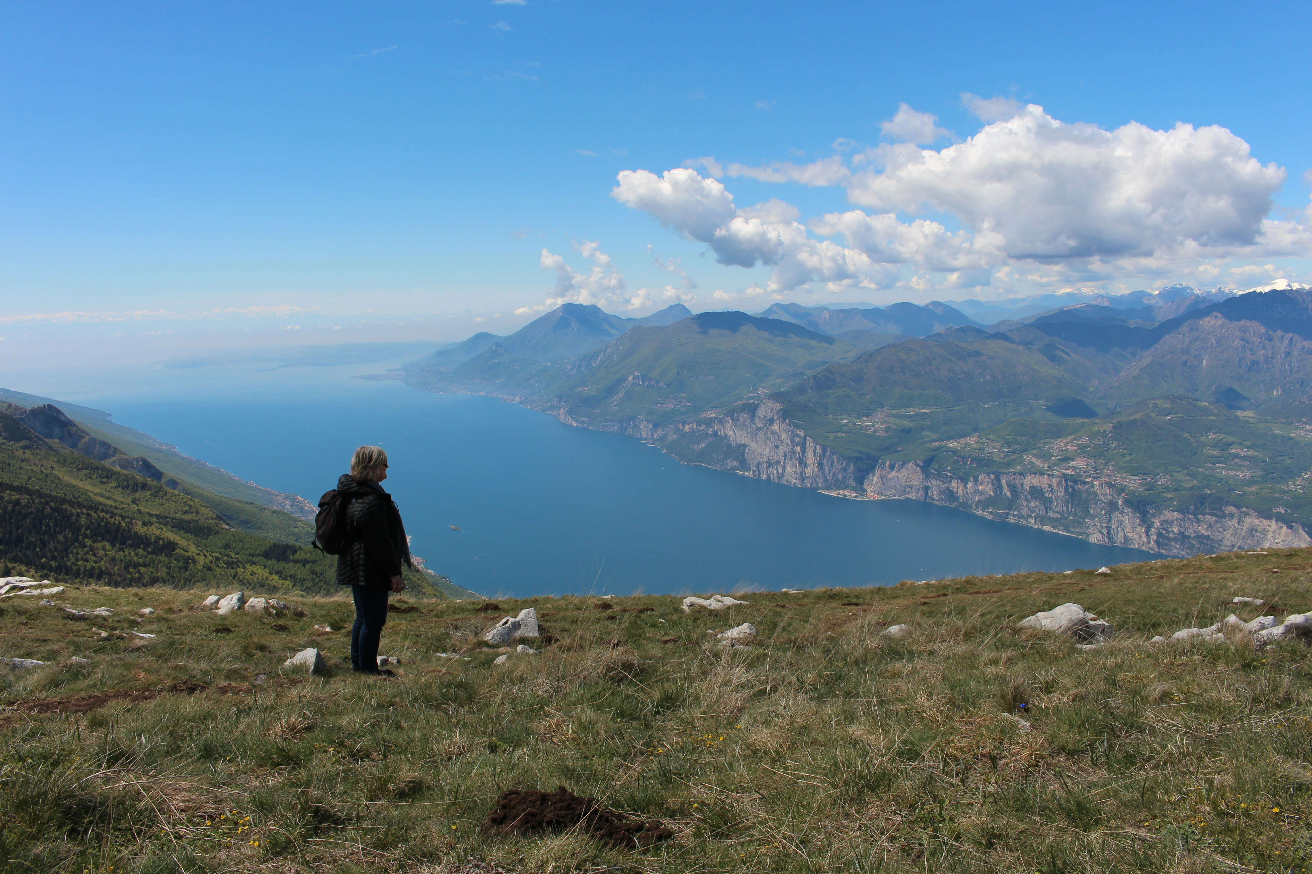 Hiker on a windswept ridge over a cobalt alpine lake beneath towering peaks