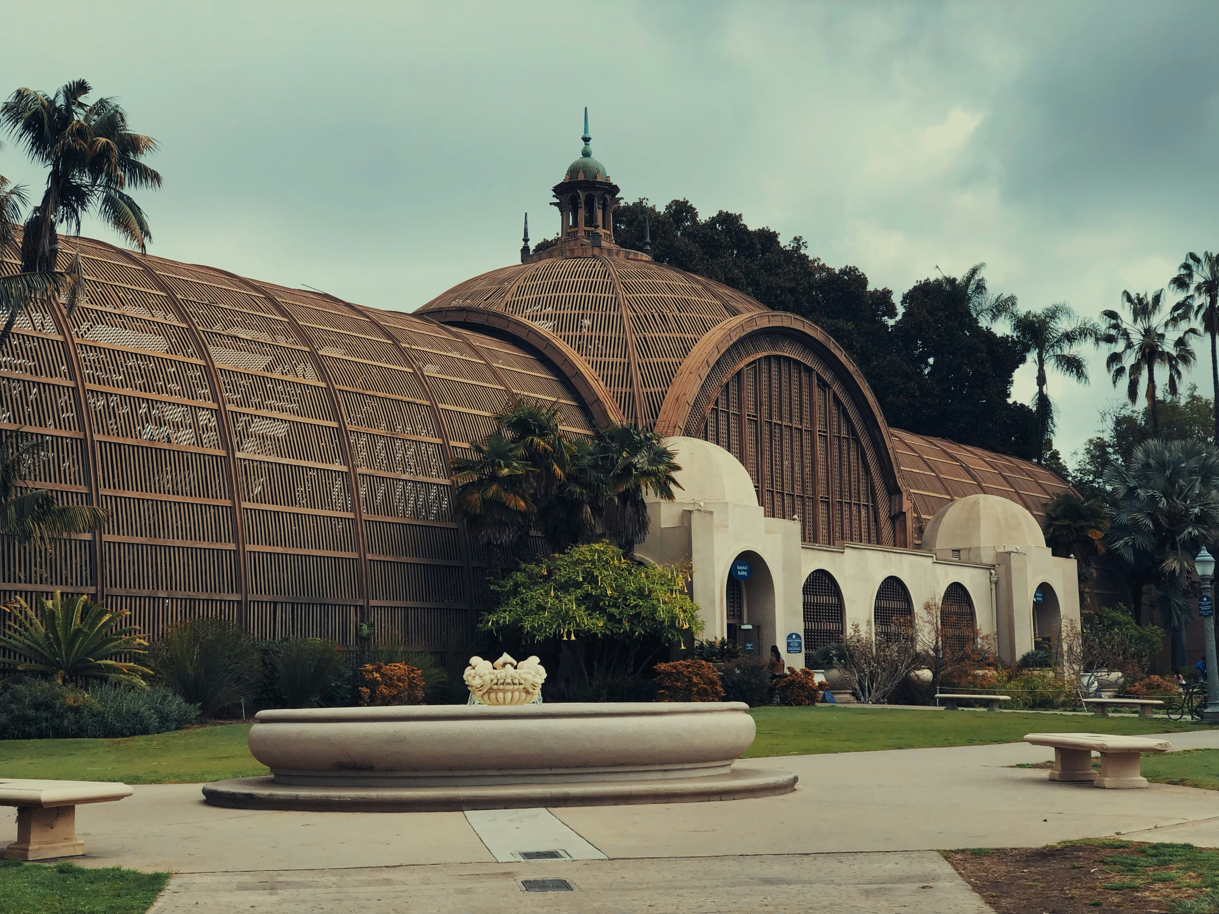 Historic botanical building with a large arched dome surrounded by lush greenery and a central water fountain.